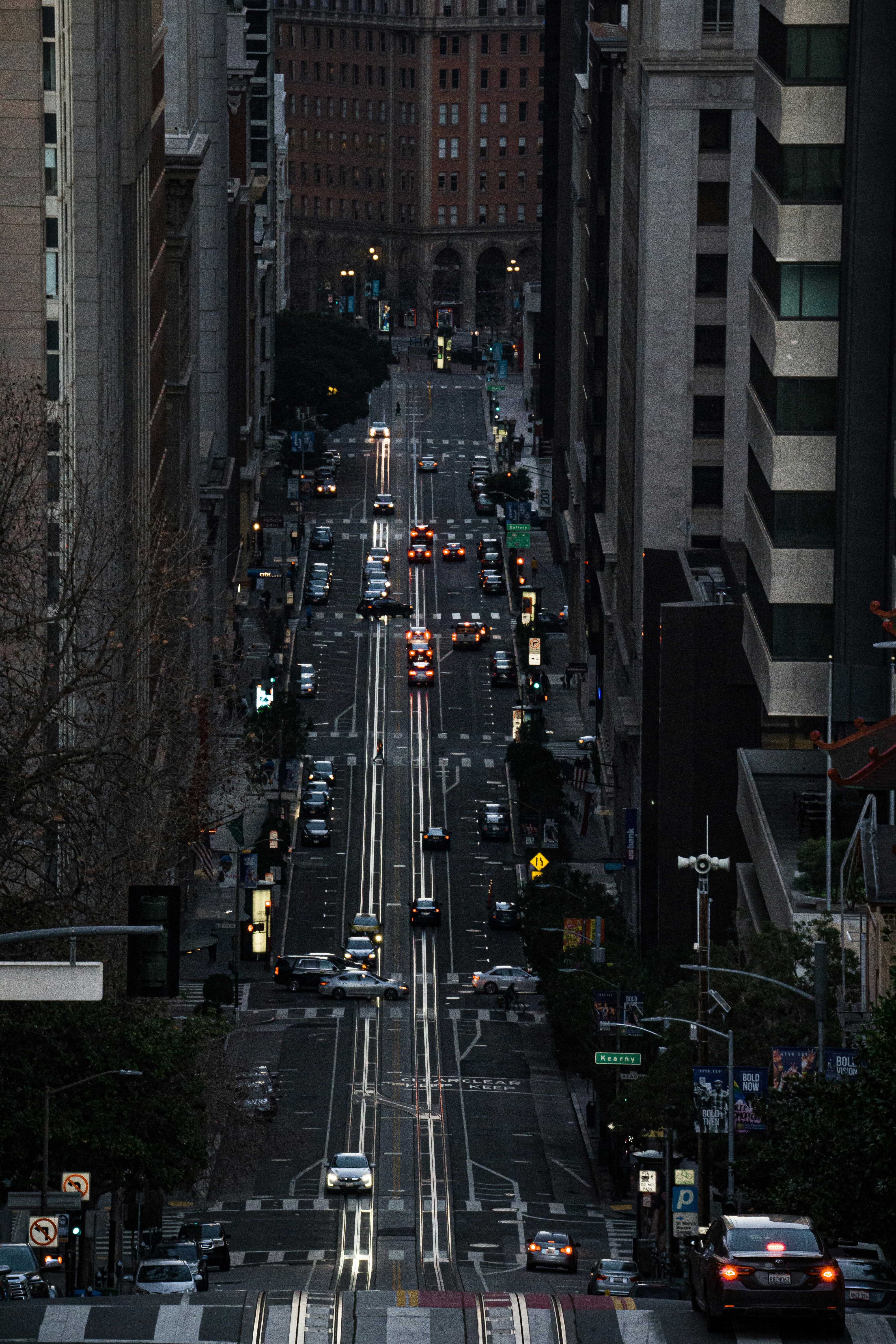 A bustling city street captured at dusk, showcasing vehicles navigating the illuminated tracks amidst towering buildings.