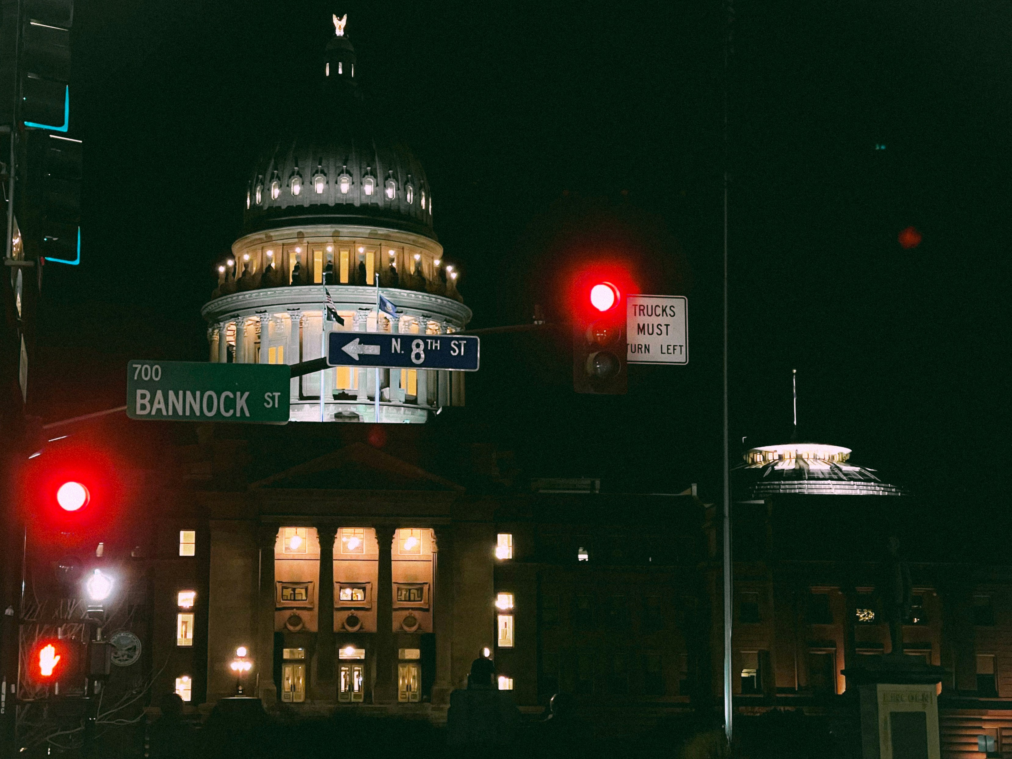 Historic building illuminated at night, with street signs directing traffic and red traffic lights glowing in the foreground.
