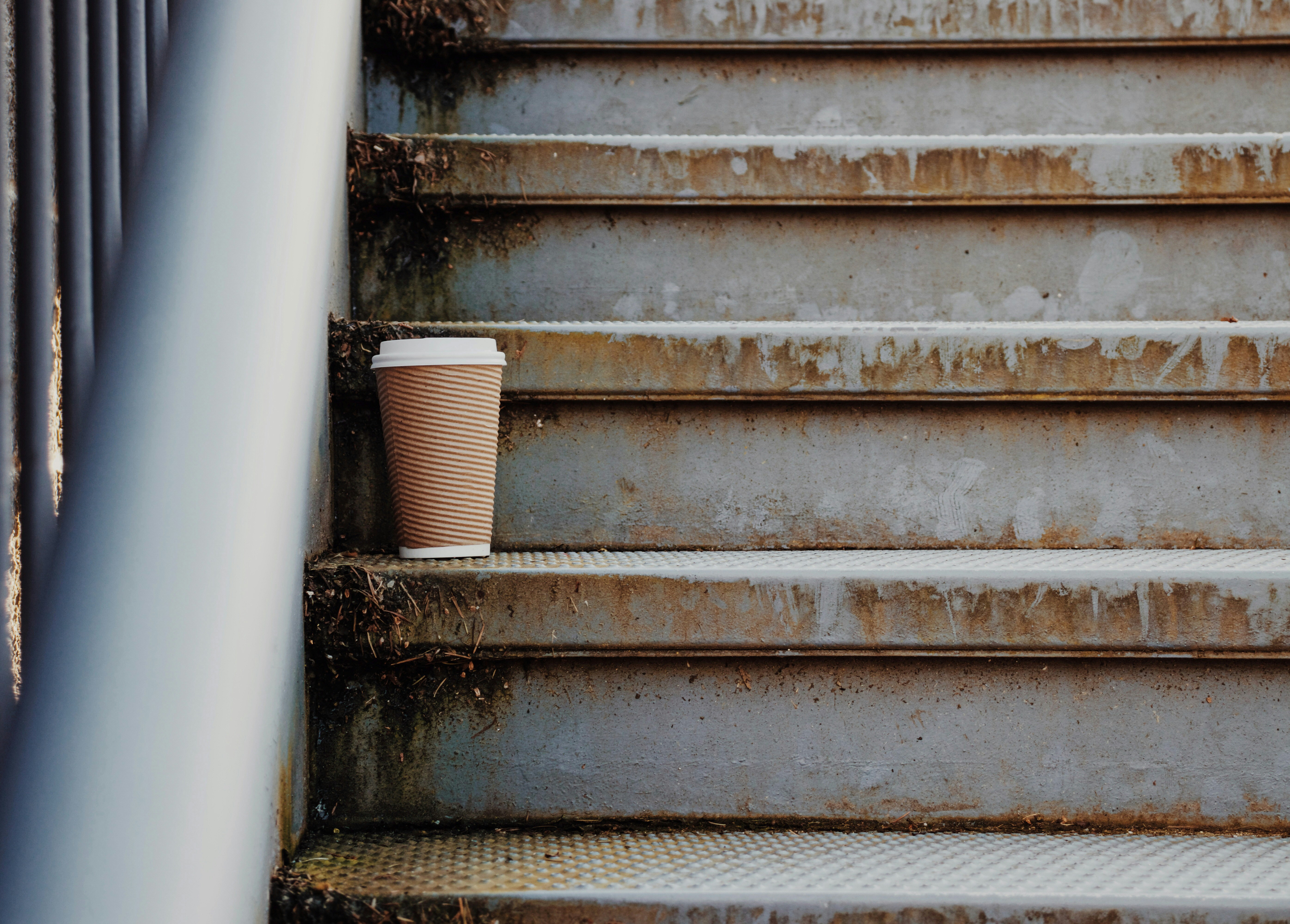 Disposable coffee cup on weathered metal stairs under soft lighting.