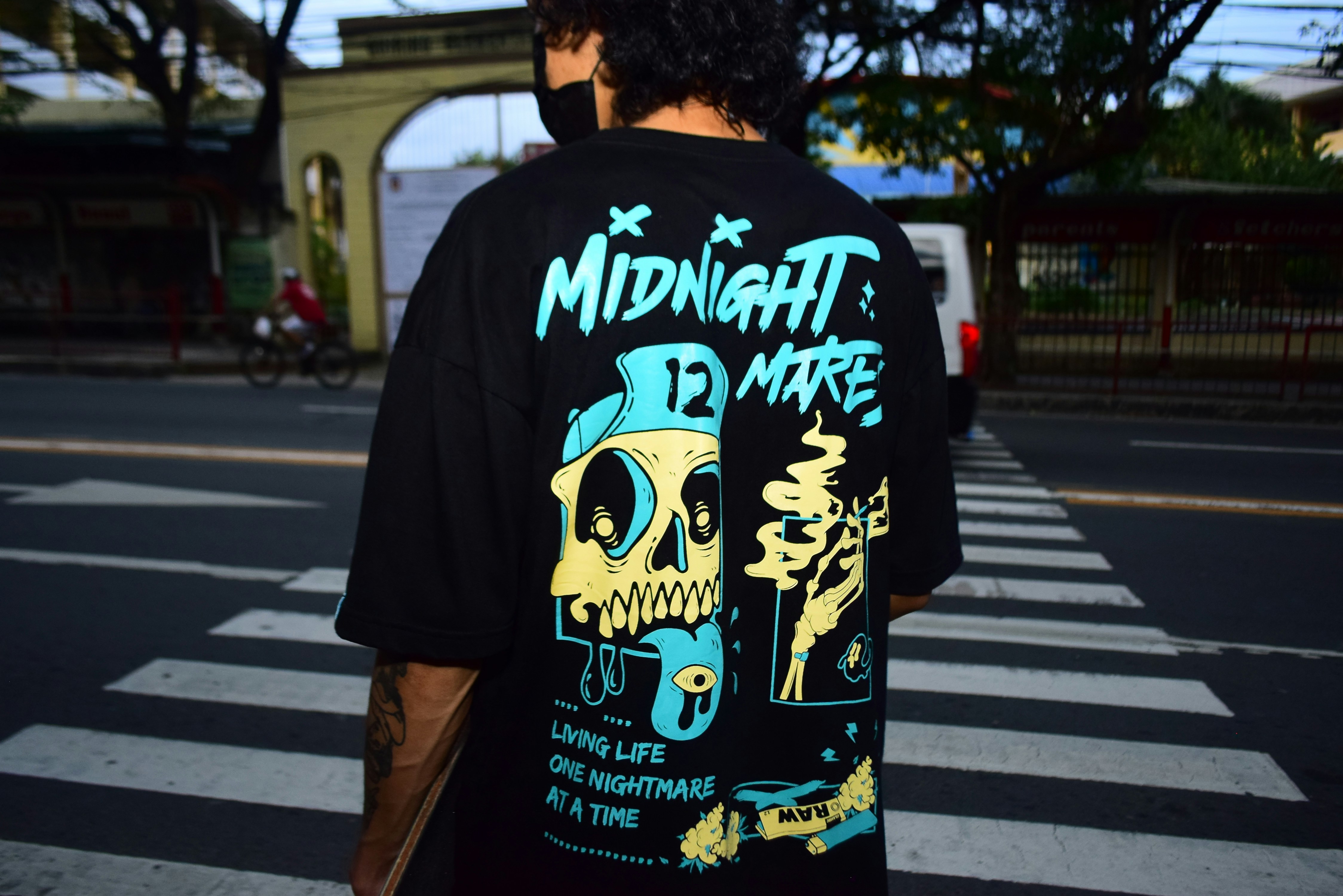 Individual wearing a black T-shirt featuring vibrant graphics of a skull and text on a busy street. The design reflects a unique streetwear aesthetic.