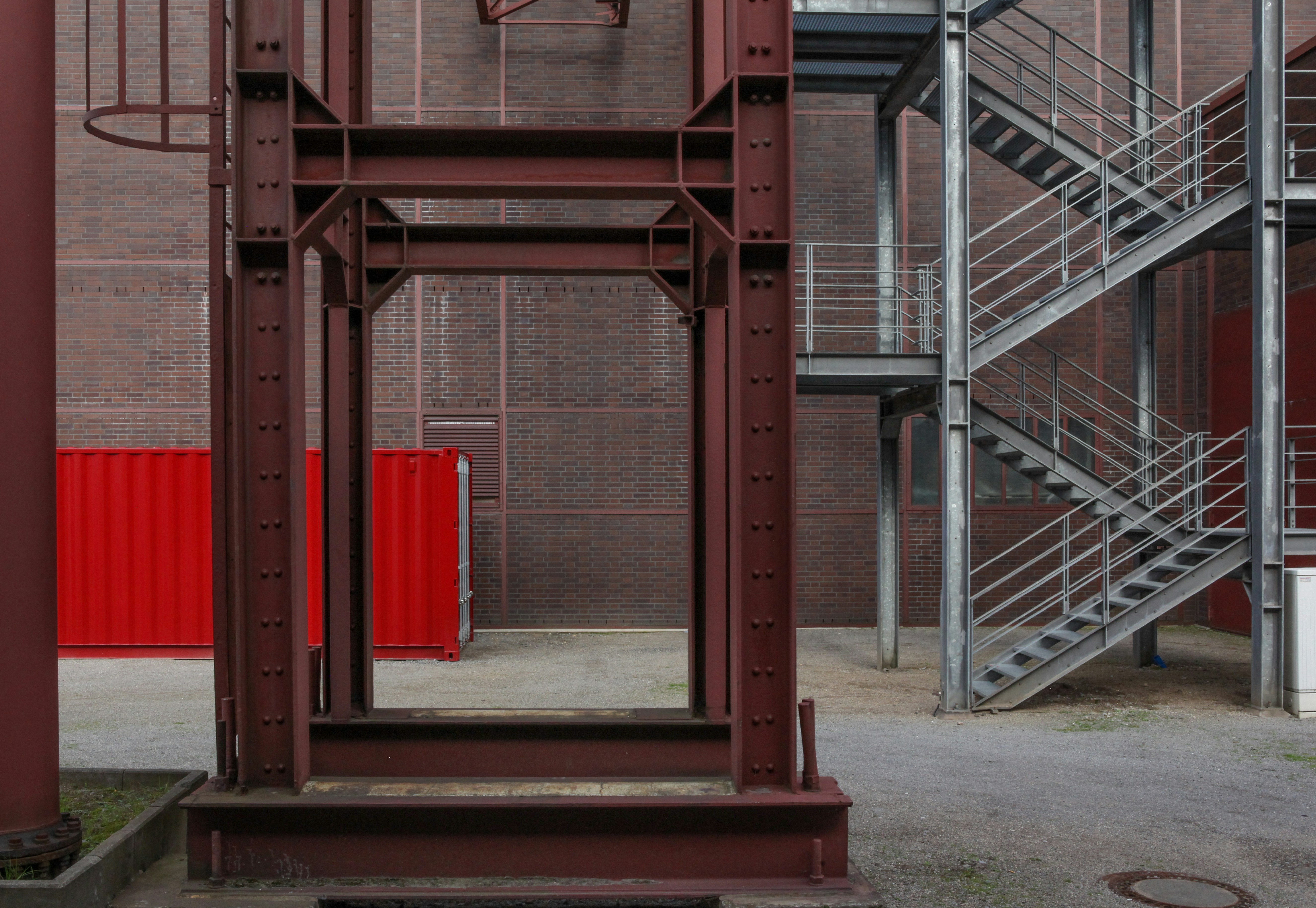 Red metal frame against a concrete floor with adjacent steel staircases and a red container.
