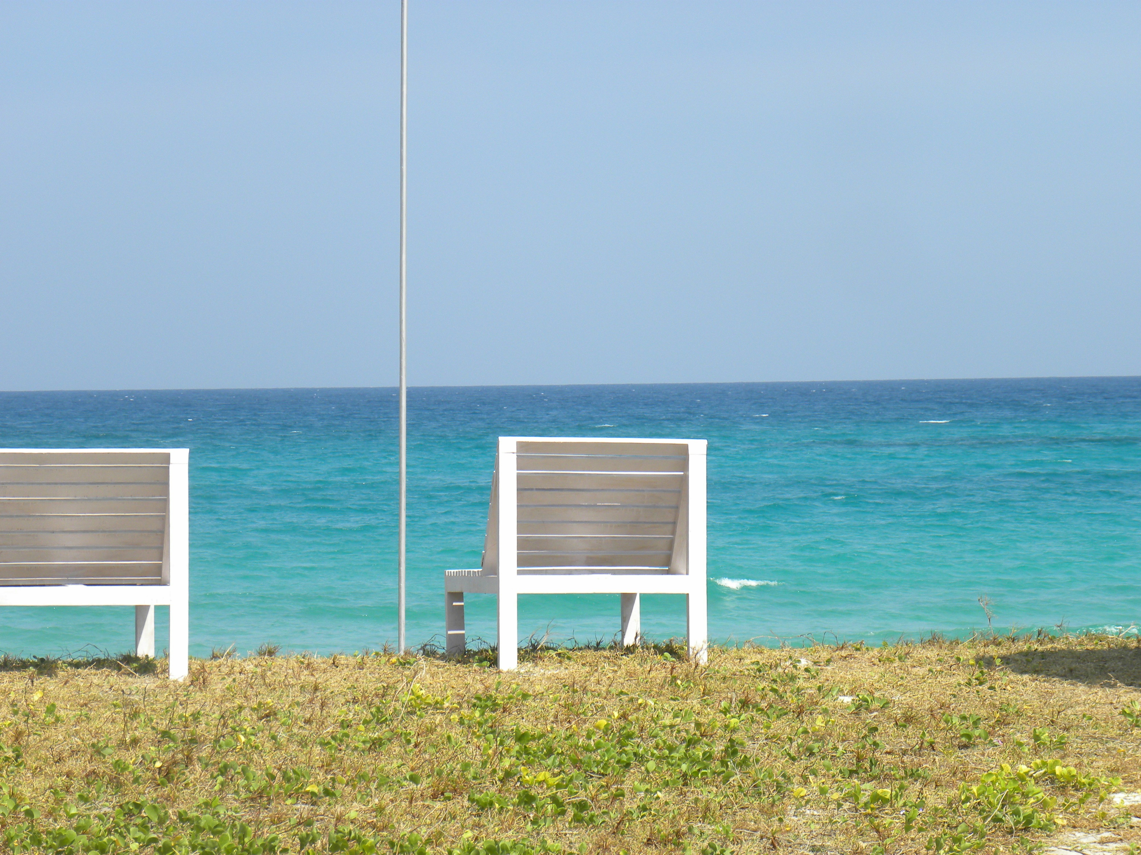 Two white benches overlooking a serene turquoise sea, inviting contemplation and relaxation.