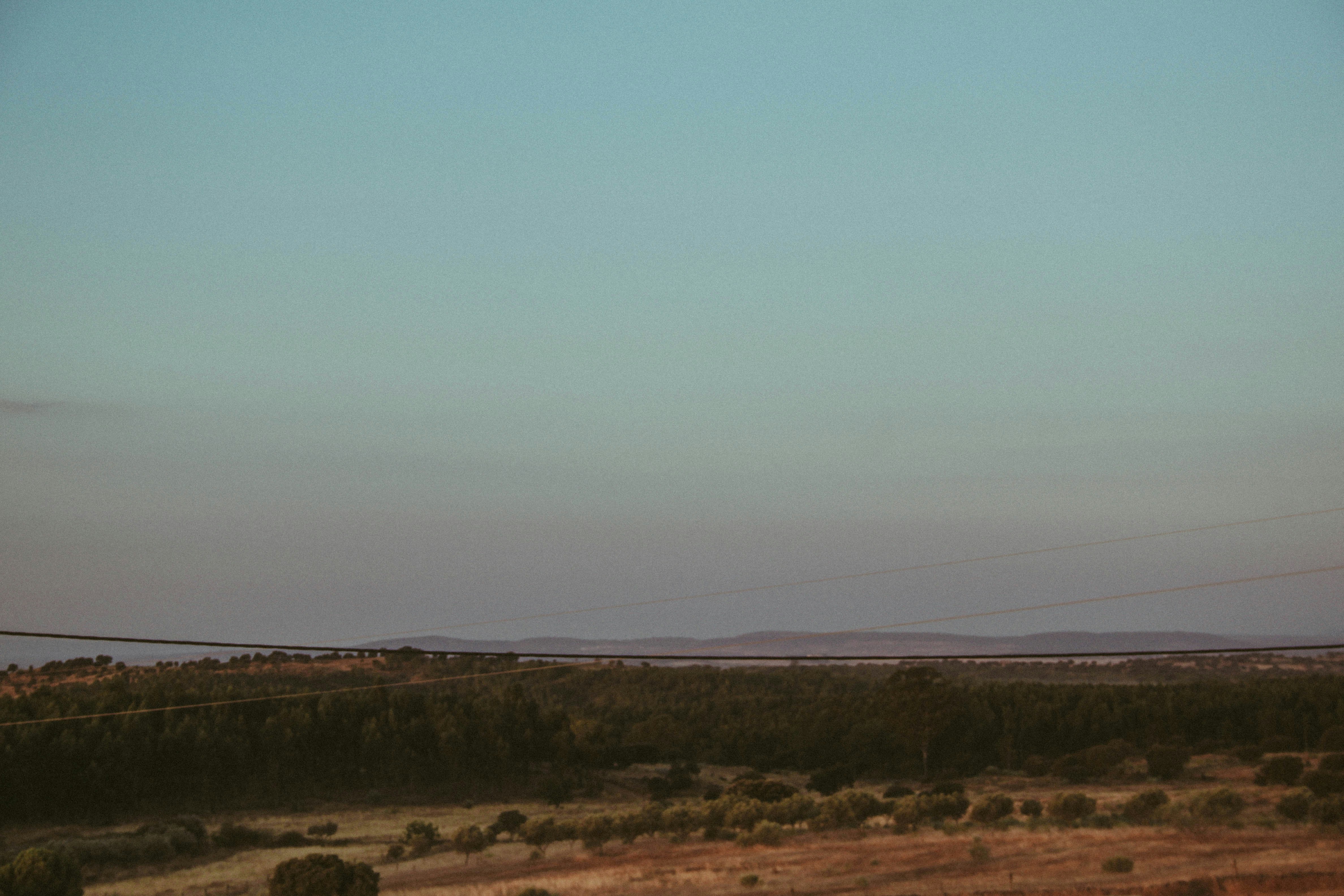 A serene landscape showcasing rolling hills under a soft blue sky, with a gentle gradient from earth to sky. The scene captures the tranquility of nature's expanse.
