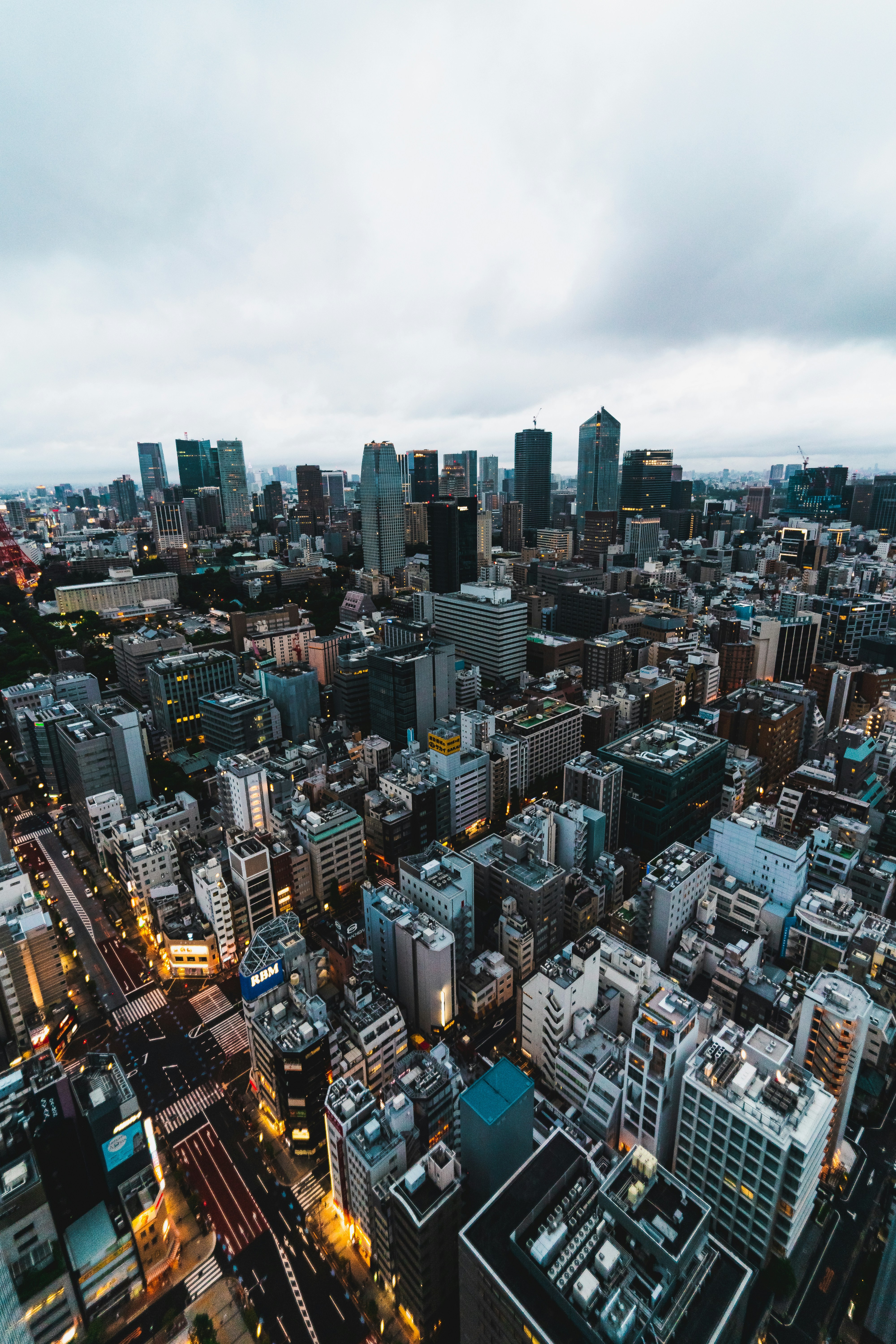 Aerial view of a bustling cityscape illuminated by streetlights, showcasing a mix of modern skyscrapers and dense urban architecture under a cloudy sky.