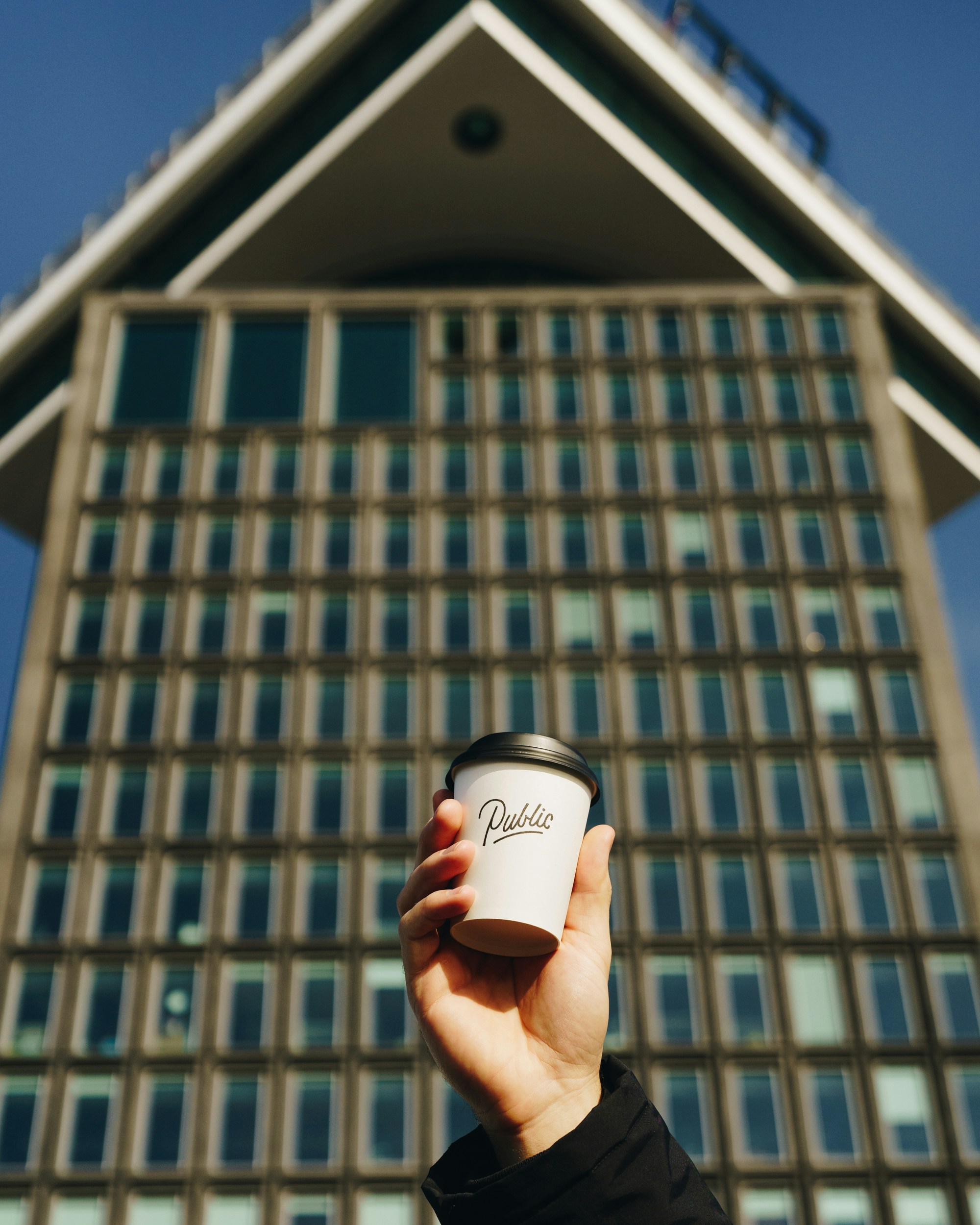 Cup in Hand Against a Glass-Grid Skyline