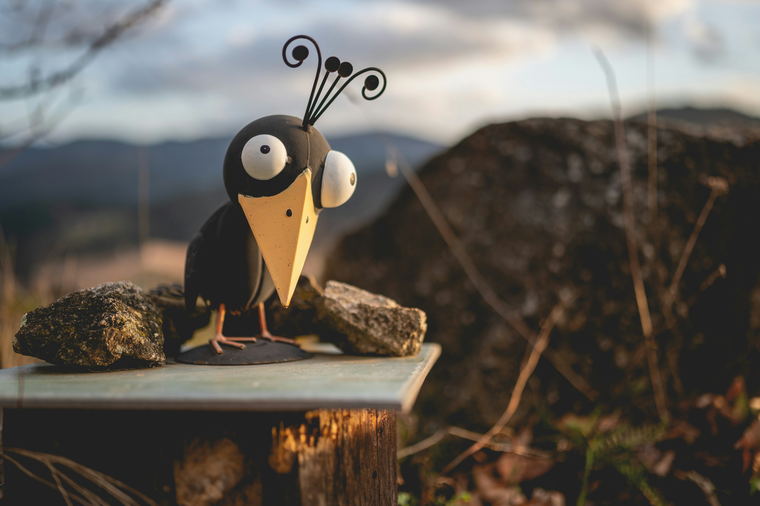 Whimsical Clay Crow on a Weathered Stump Against Mountain Light