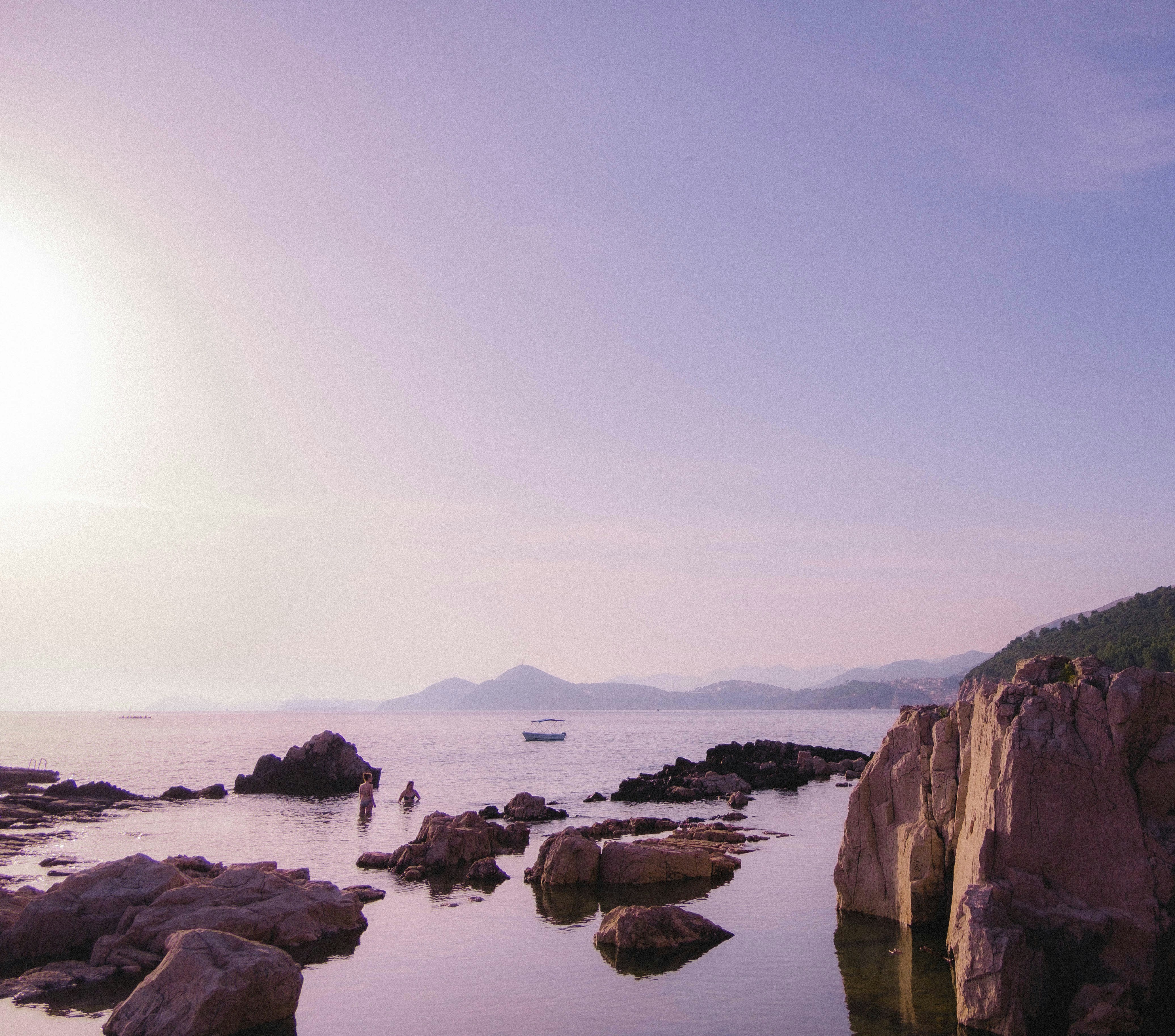 Sunlit Coastal Mosaic: Rocks, Water, and Distant Boats at Dusk