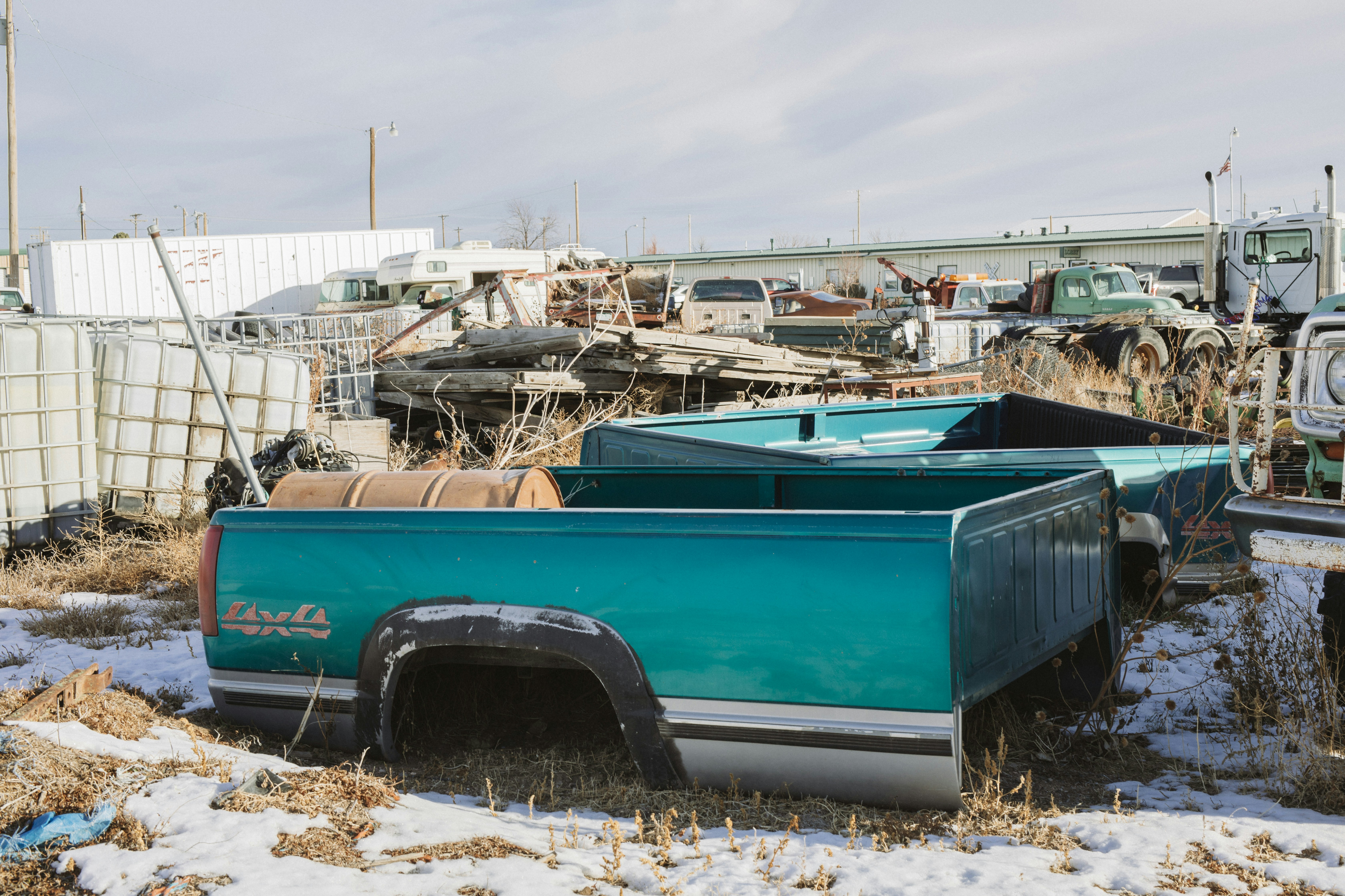 Deserted teal truck bed among scrapyard remnants