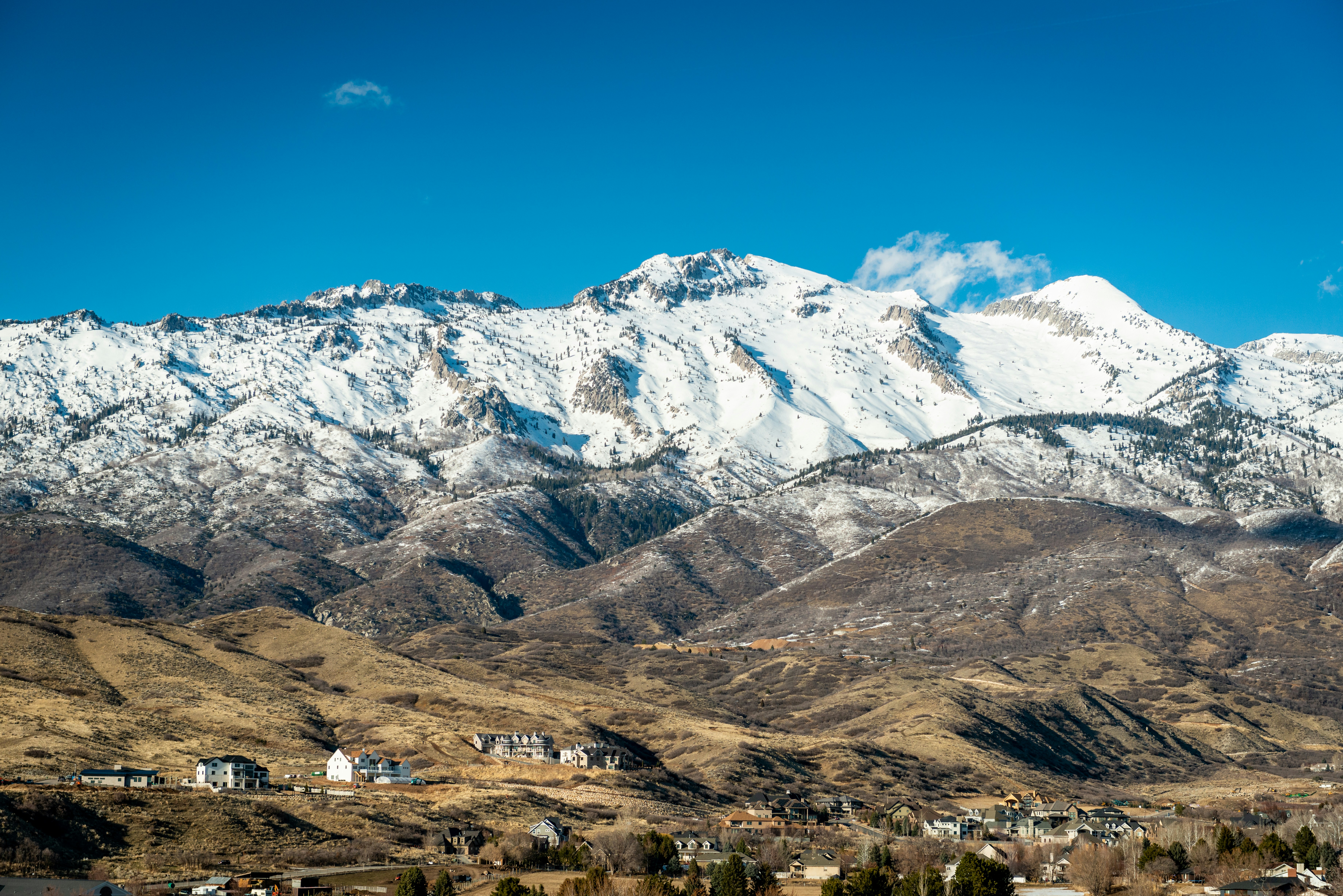 Snow-covered mountains rise above a dry, rugged landscape under a bright blue sky.