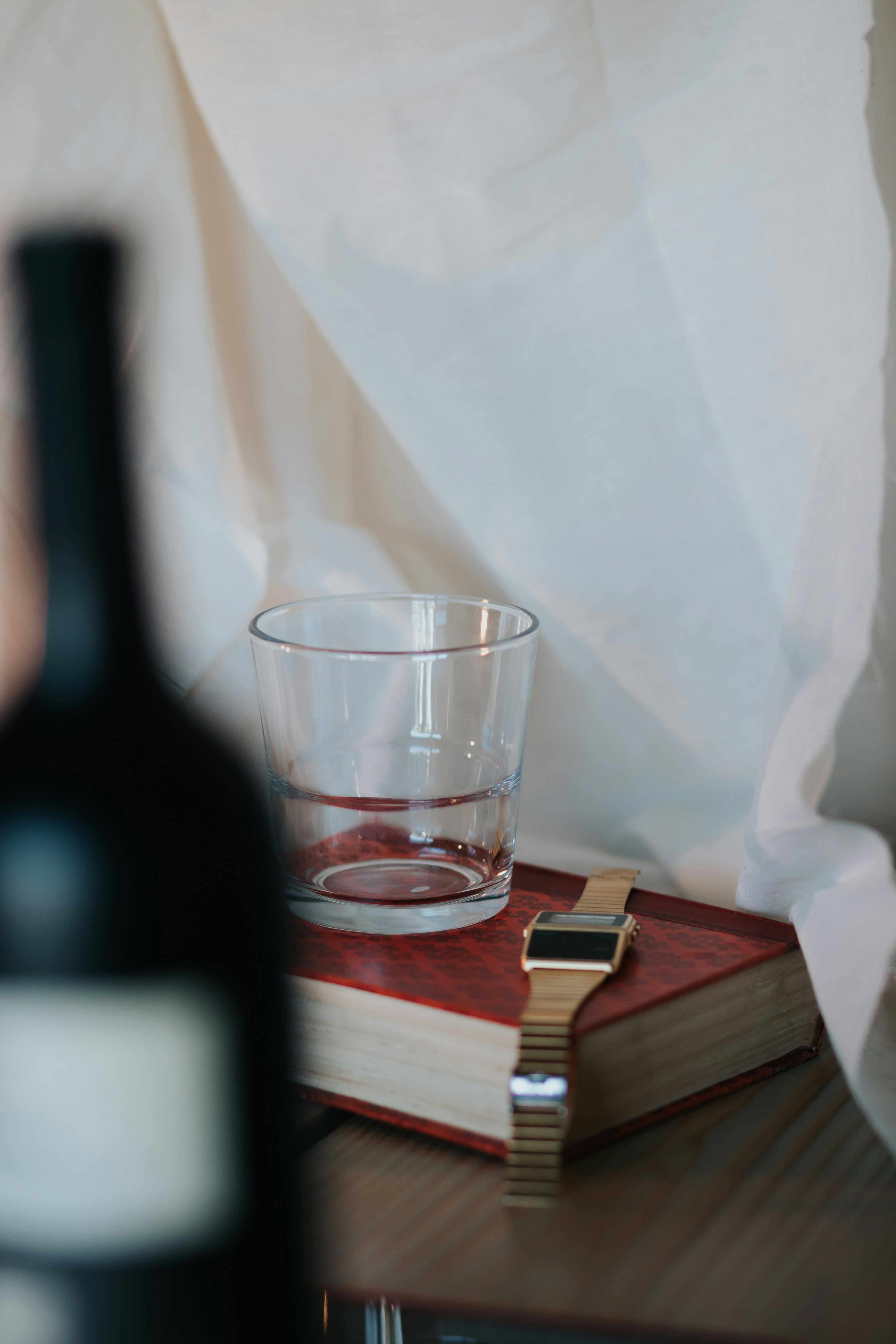 Still Life of Quiet Glass: A Bottle, Book, and Watch Resting by White Drapery