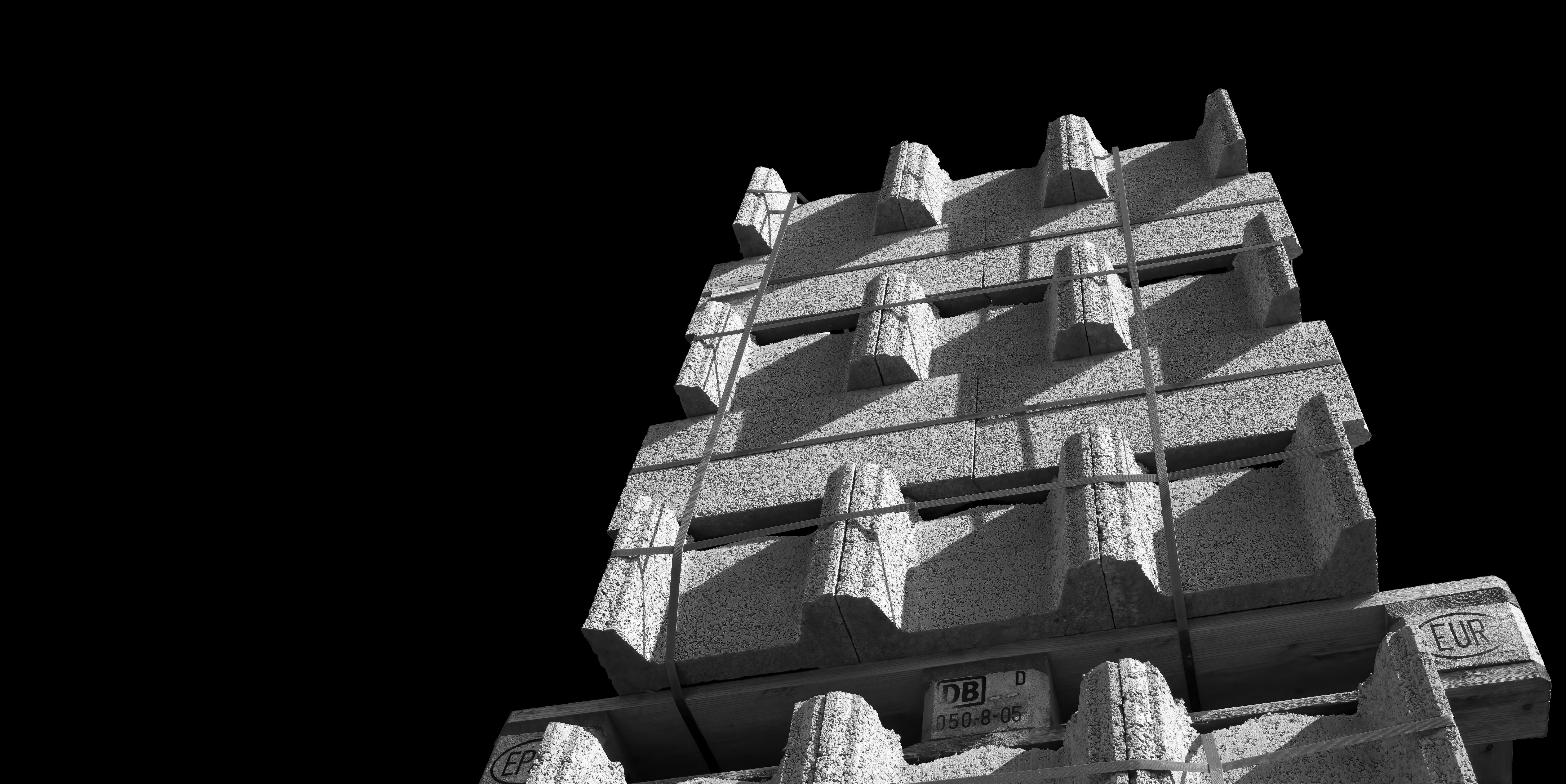 A towering stack of concrete blocks against a stark black background, emphasizing their geometric design and texture.