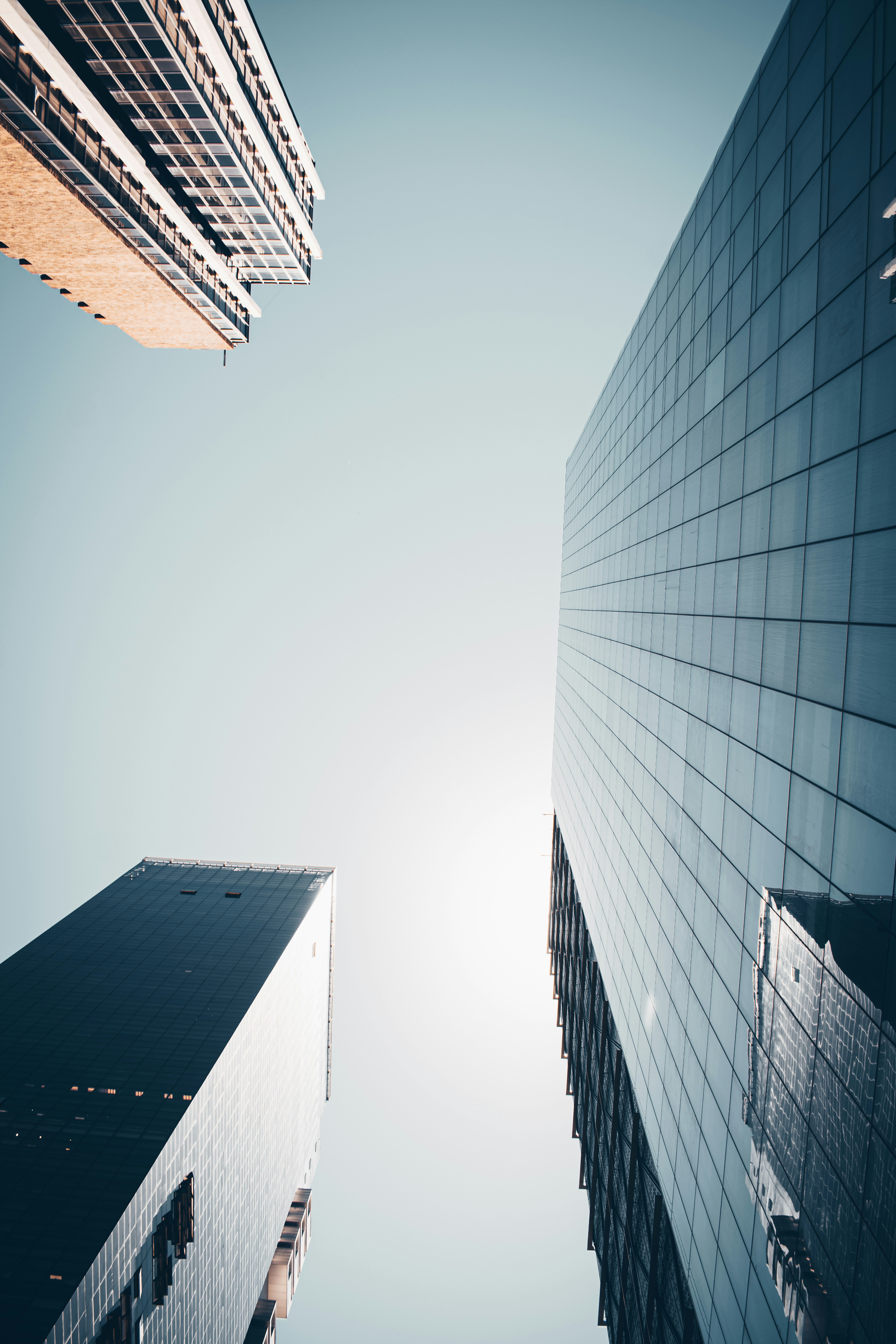 Skyscrapers reaching towards the sky, captured from a low angle, showcasing their reflective surfaces against a clear blue backdrop.