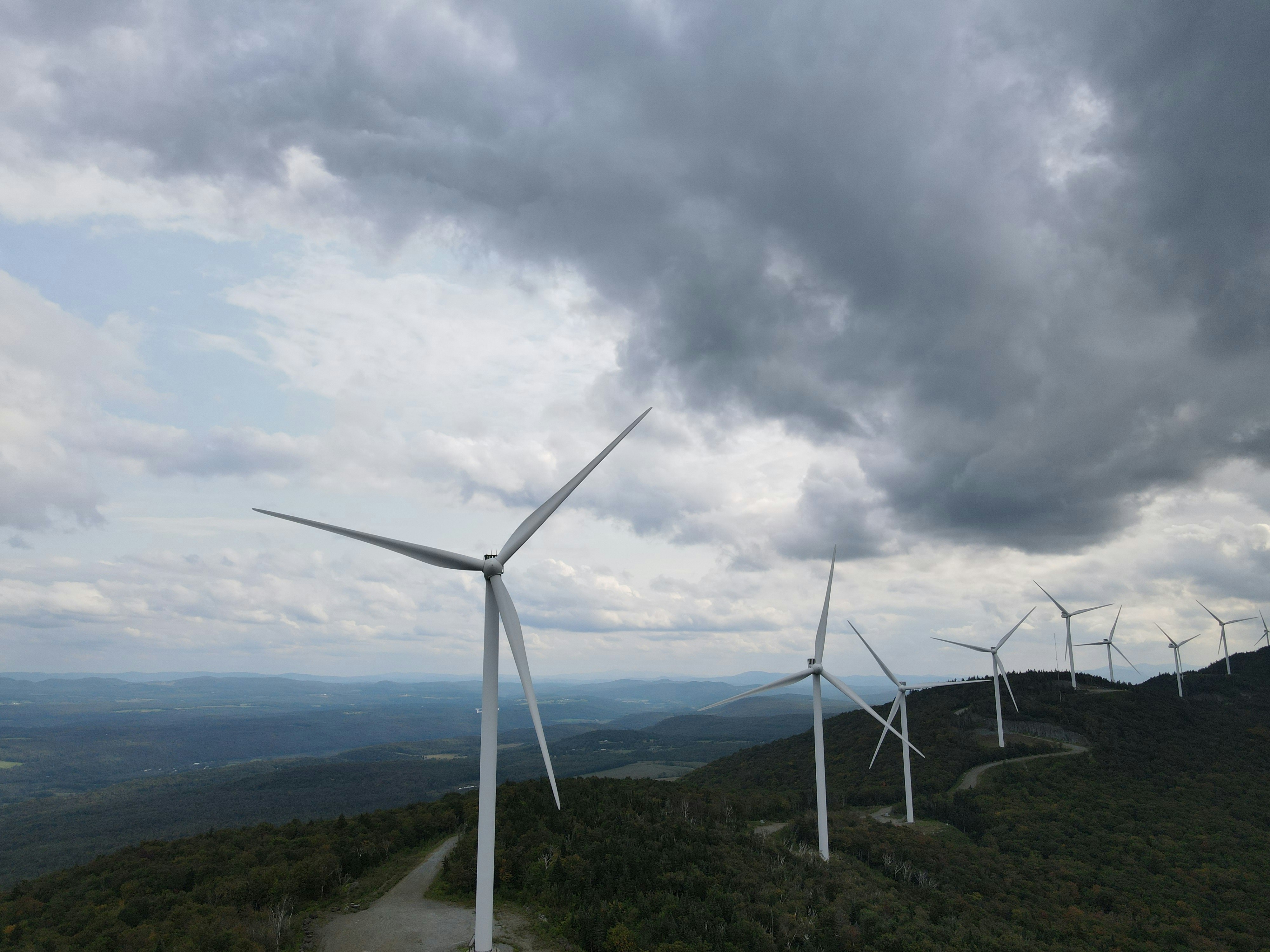 Wind turbines stand tall against a backdrop of rolling hills and dramatic clouds, showcasing renewable energy in harmony with nature.