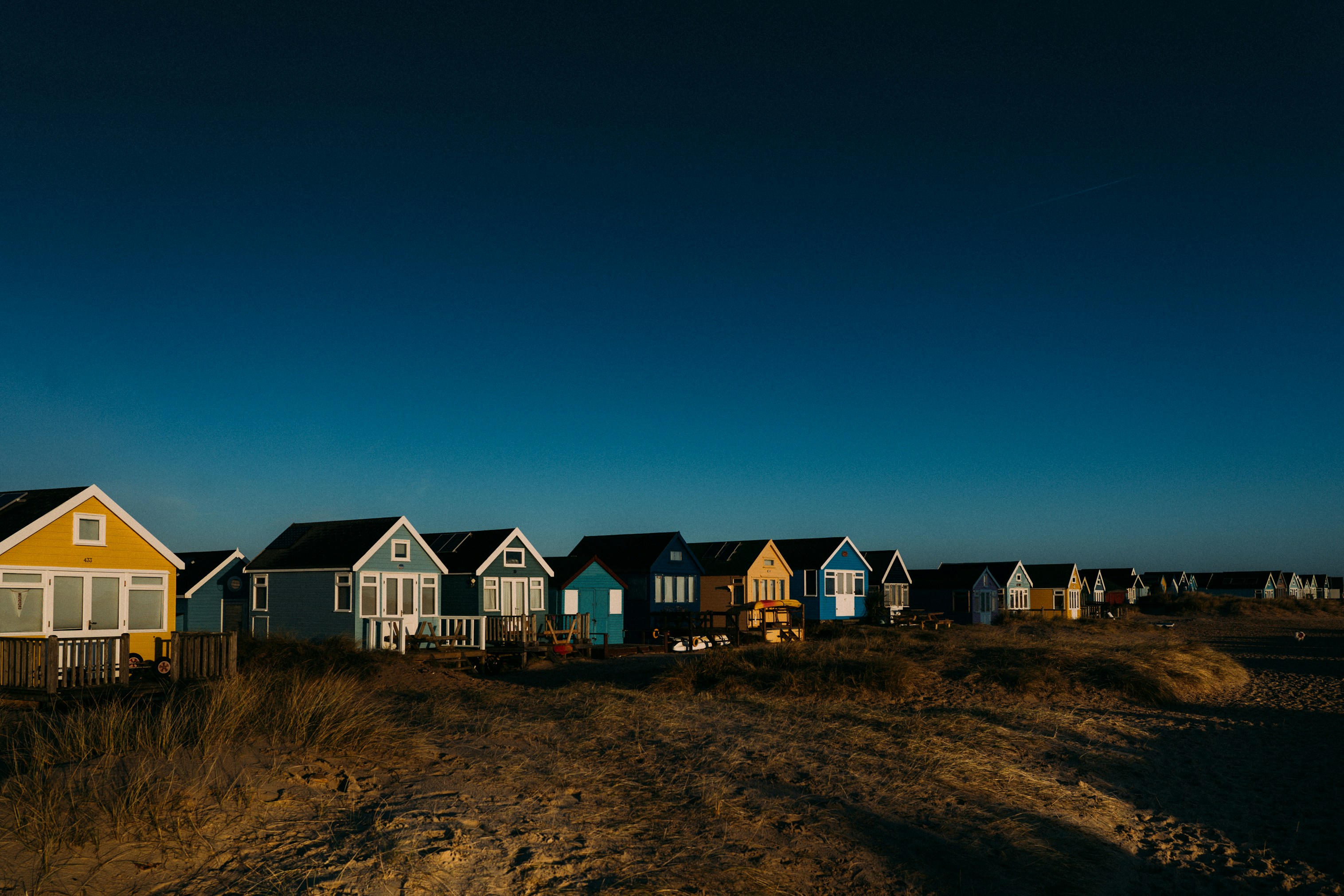 Row of vibrant beach houses lined along a sandy path under a deep blue sky at dusk.