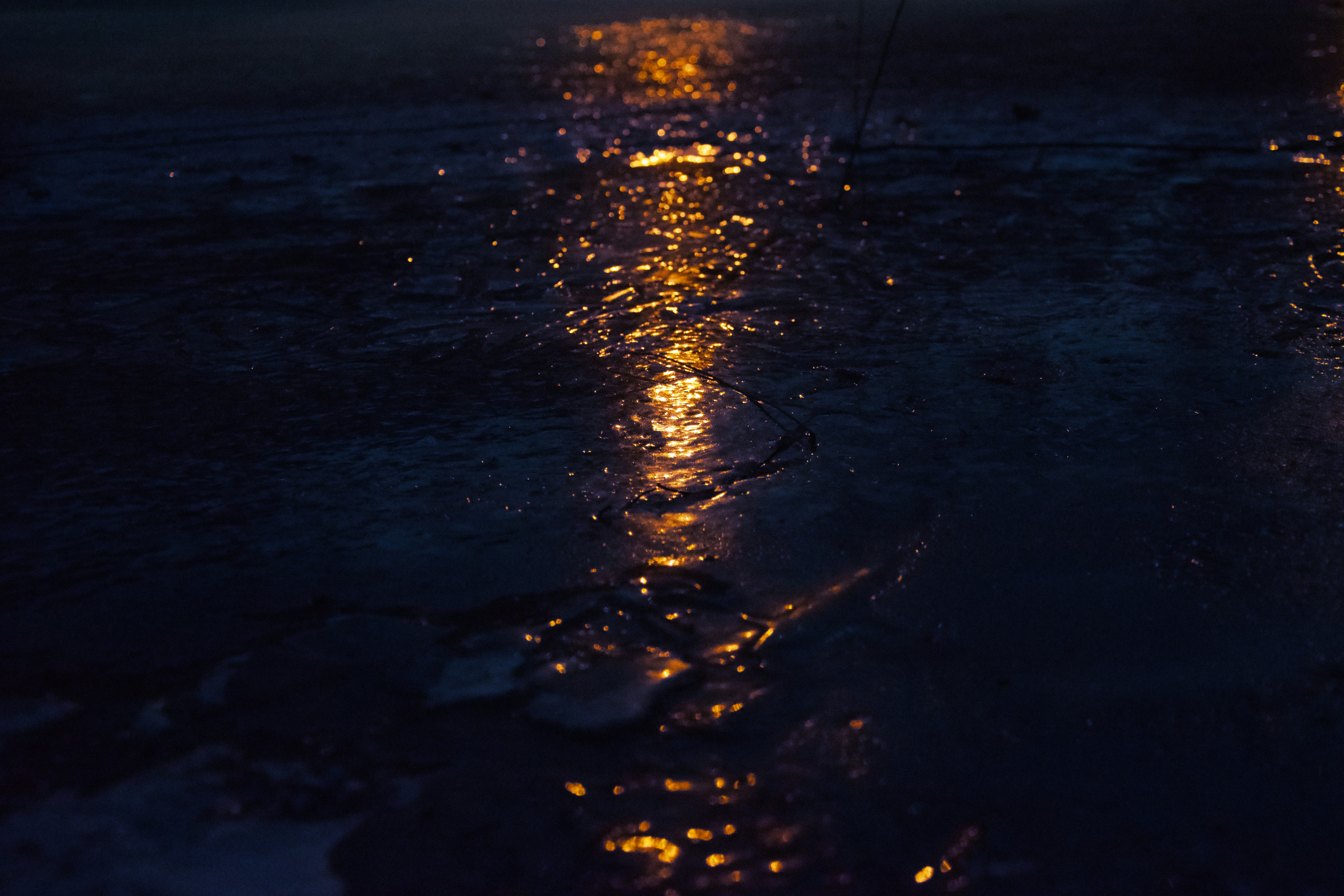 Golden reflections shimmering on a frozen surface under the night sky. The interplay of light and texture creates a serene, atmospheric scene.