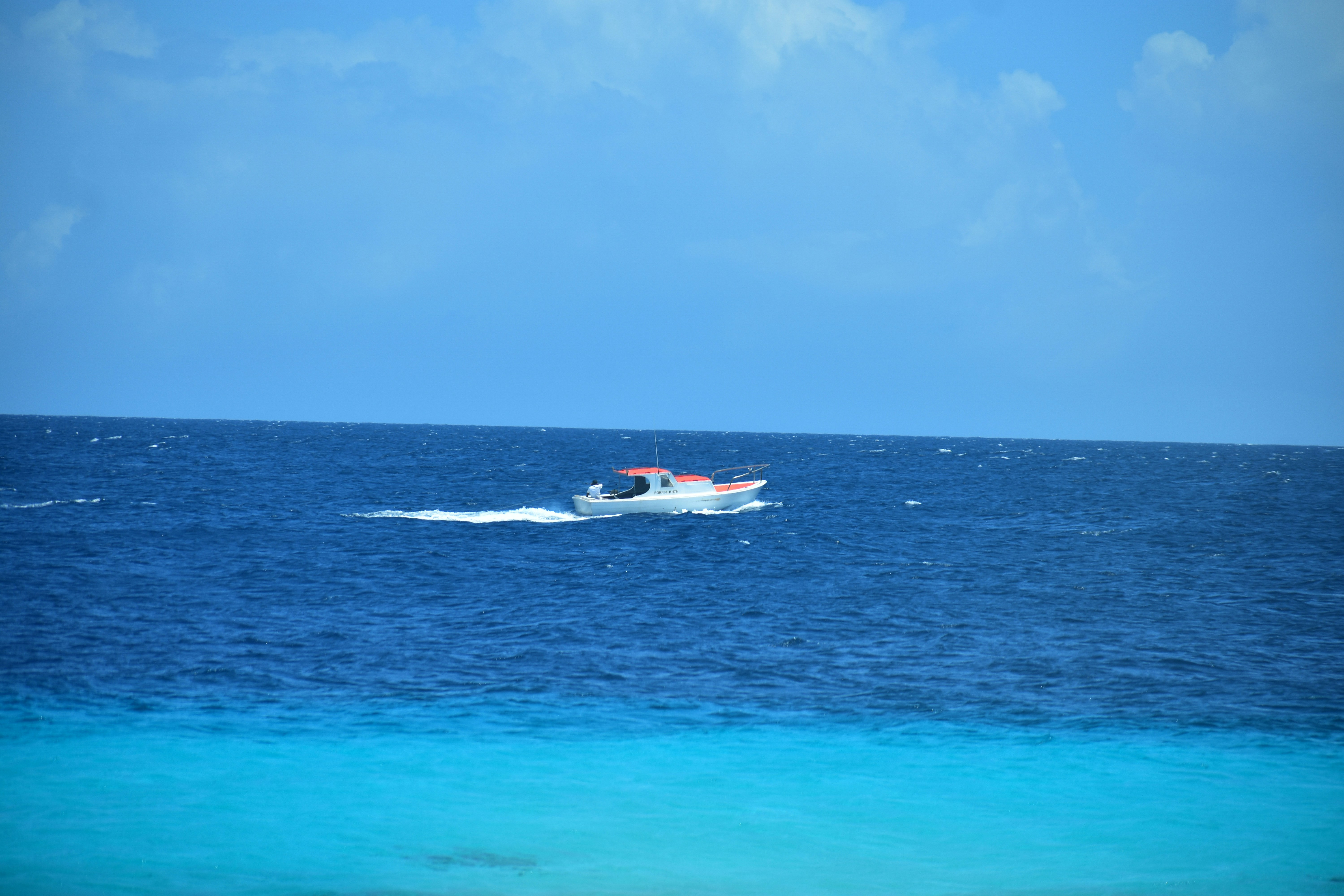 A motorboat glides through the vibrant turquoise sea, leaving a white wake against the deep blue water under a clear sky.