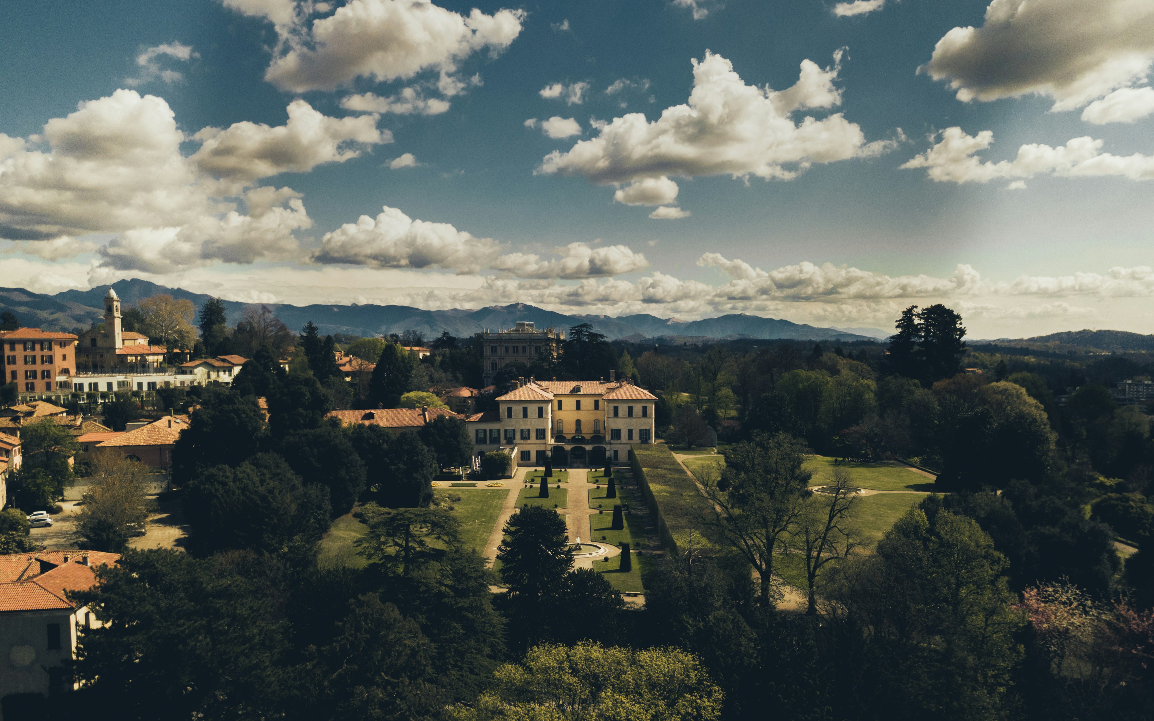 Aerial view of an elegant estate surrounded by lush gardens and distant mountains, showcasing the harmony between architecture and nature.