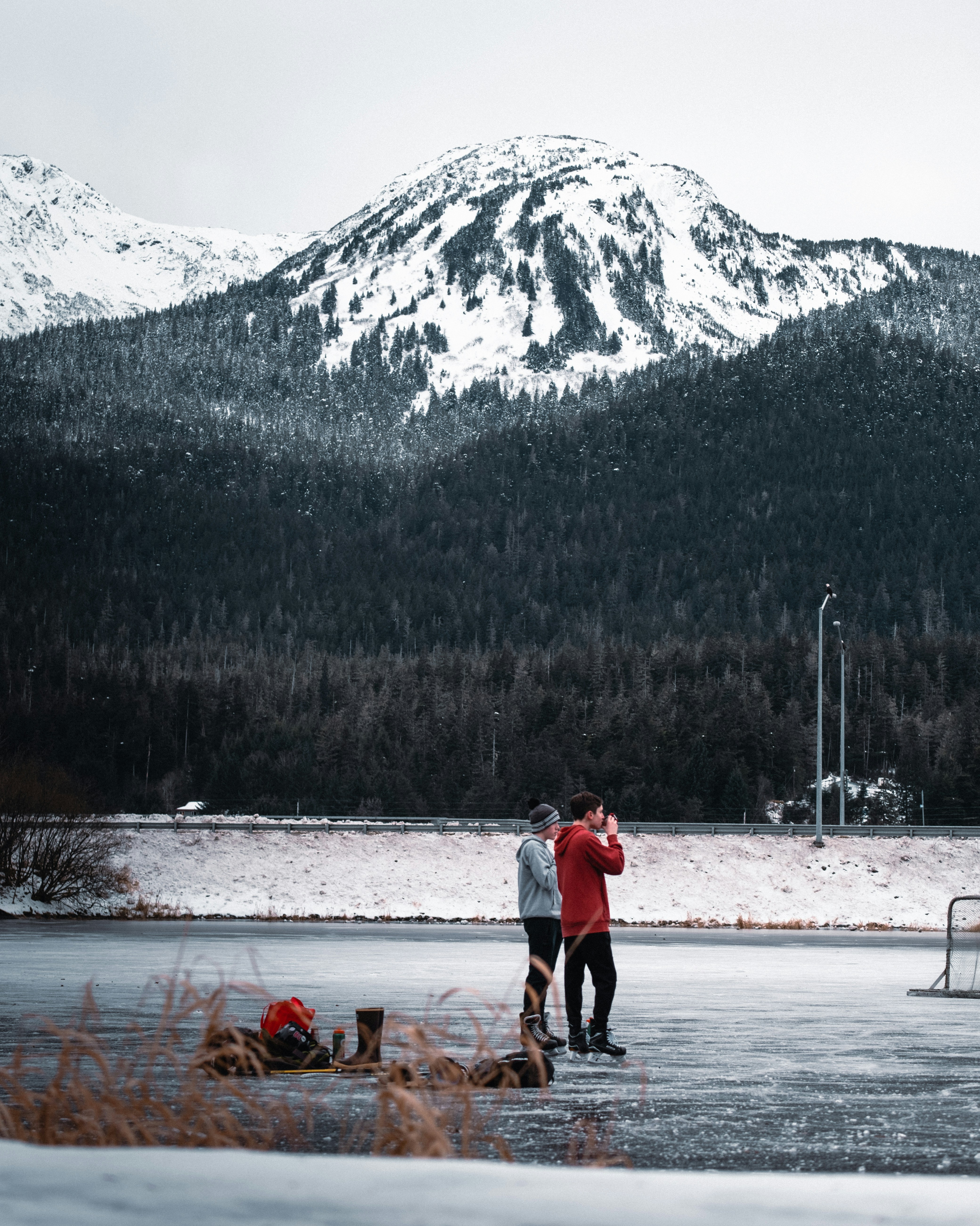 Two individuals enjoying a winter day on a frozen lake, surrounded by snow-capped mountains and evergreen trees. The scene captures the essence of outdoor leisure in a serene landscape.
