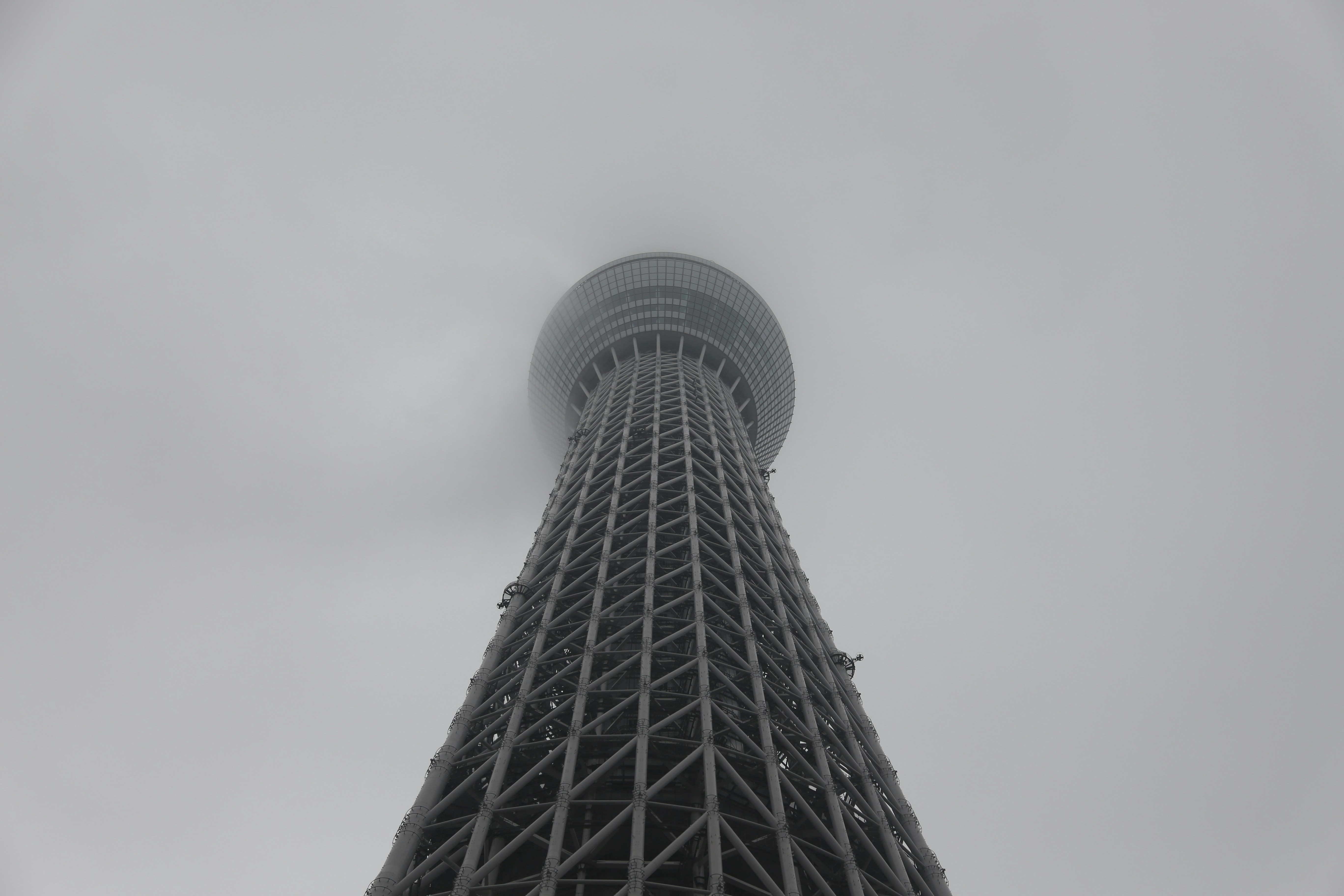 A towering structure disappearing into a blanket of clouds, showcasing modern architecture against a moody sky.