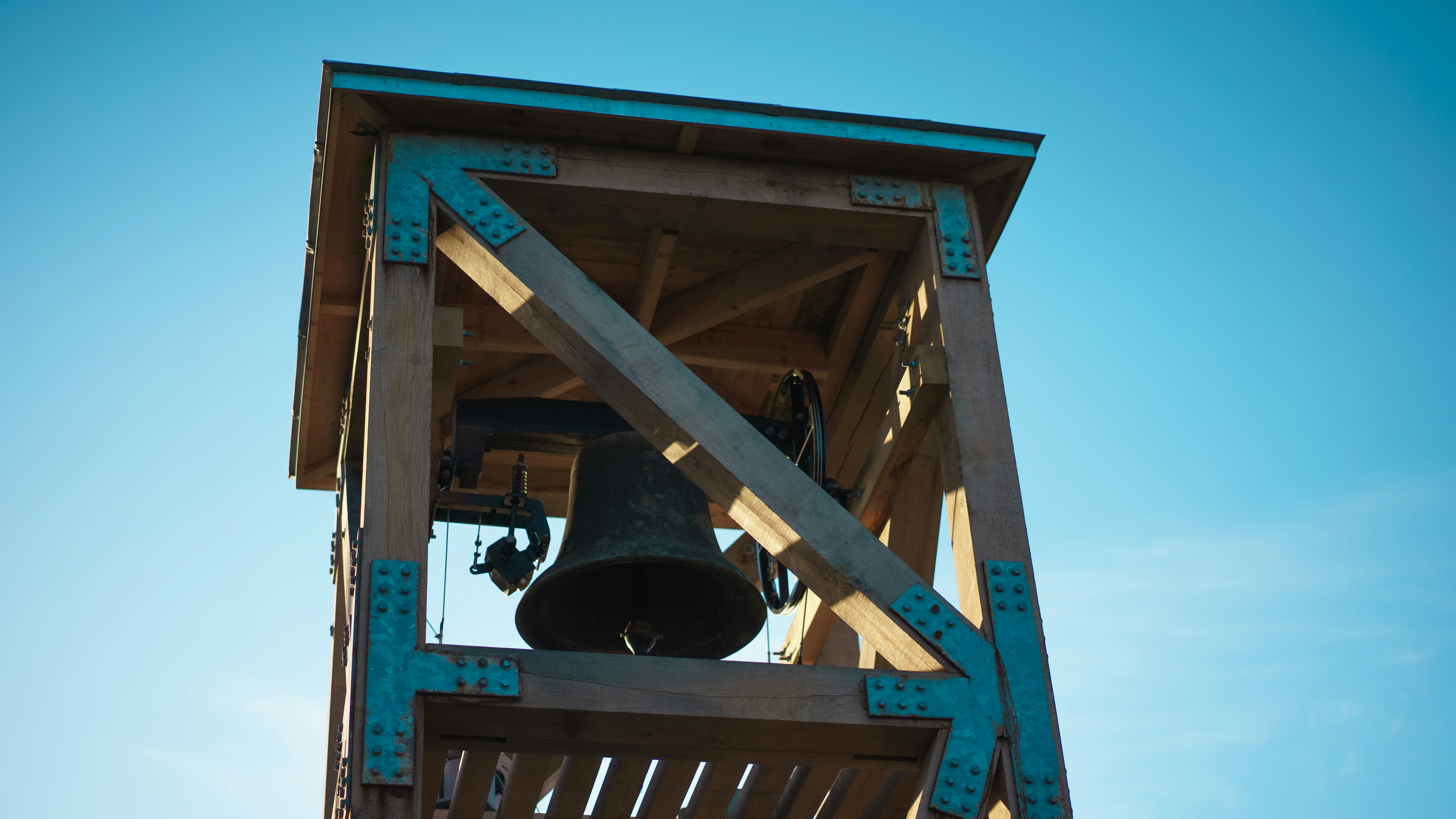 Wooden bell tower showcasing a large bell, framed by a clear blue sky. The structure highlights craftsmanship and historical significance.