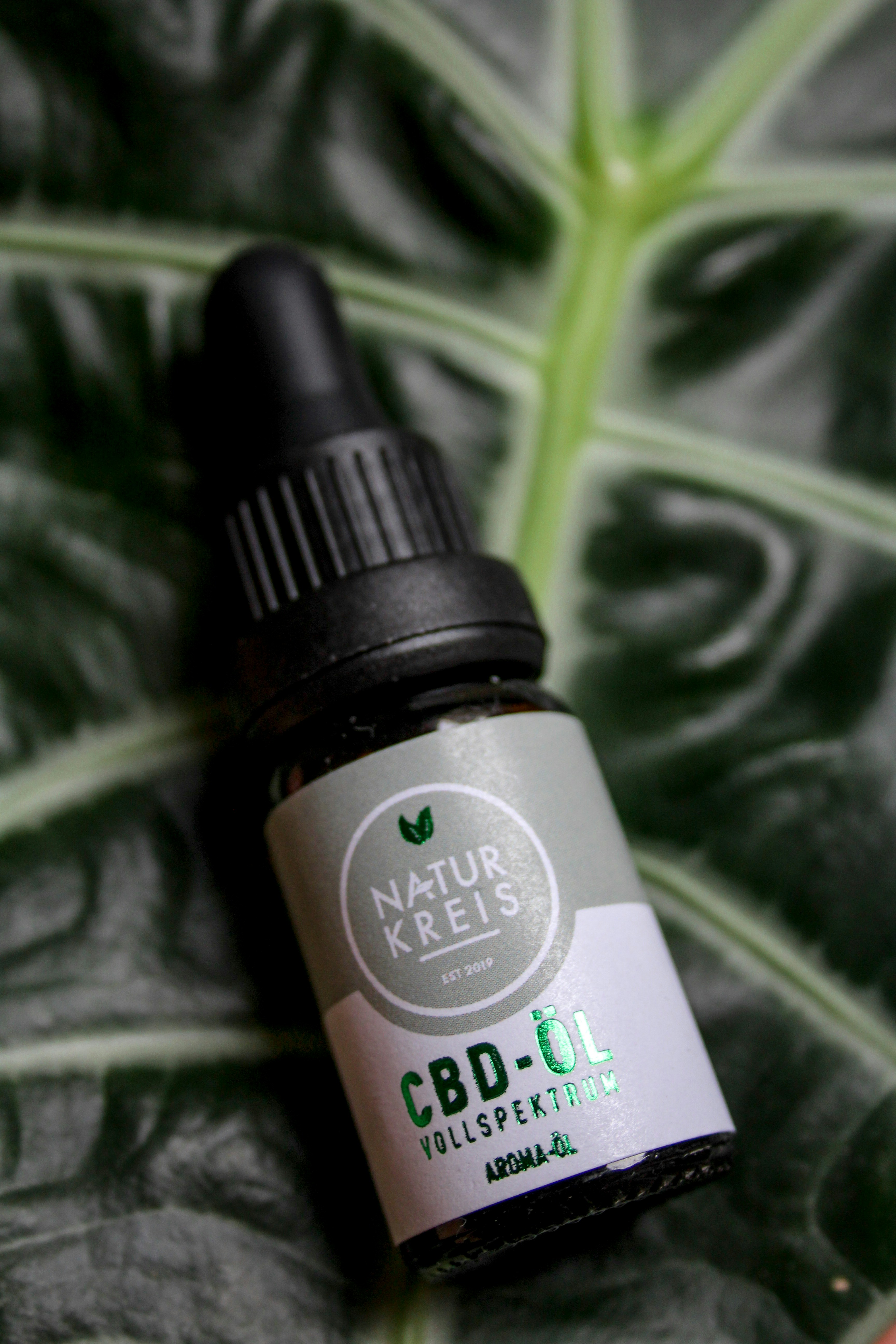 A dropper bottle of CBD oil resting on a lush green leaf, highlighting the product's natural origins.