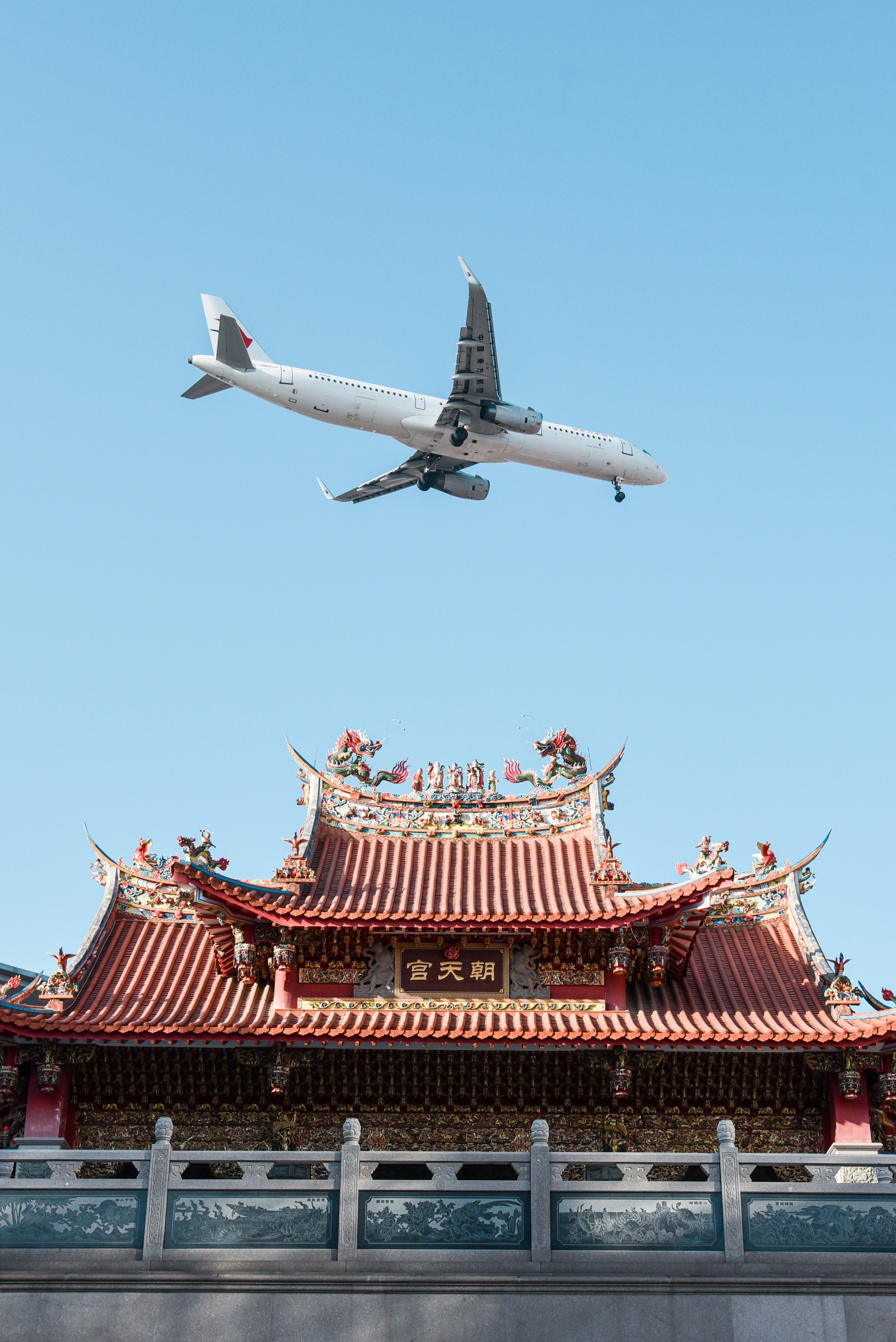 Airliner in descent over a traditional temple roof at blue sky