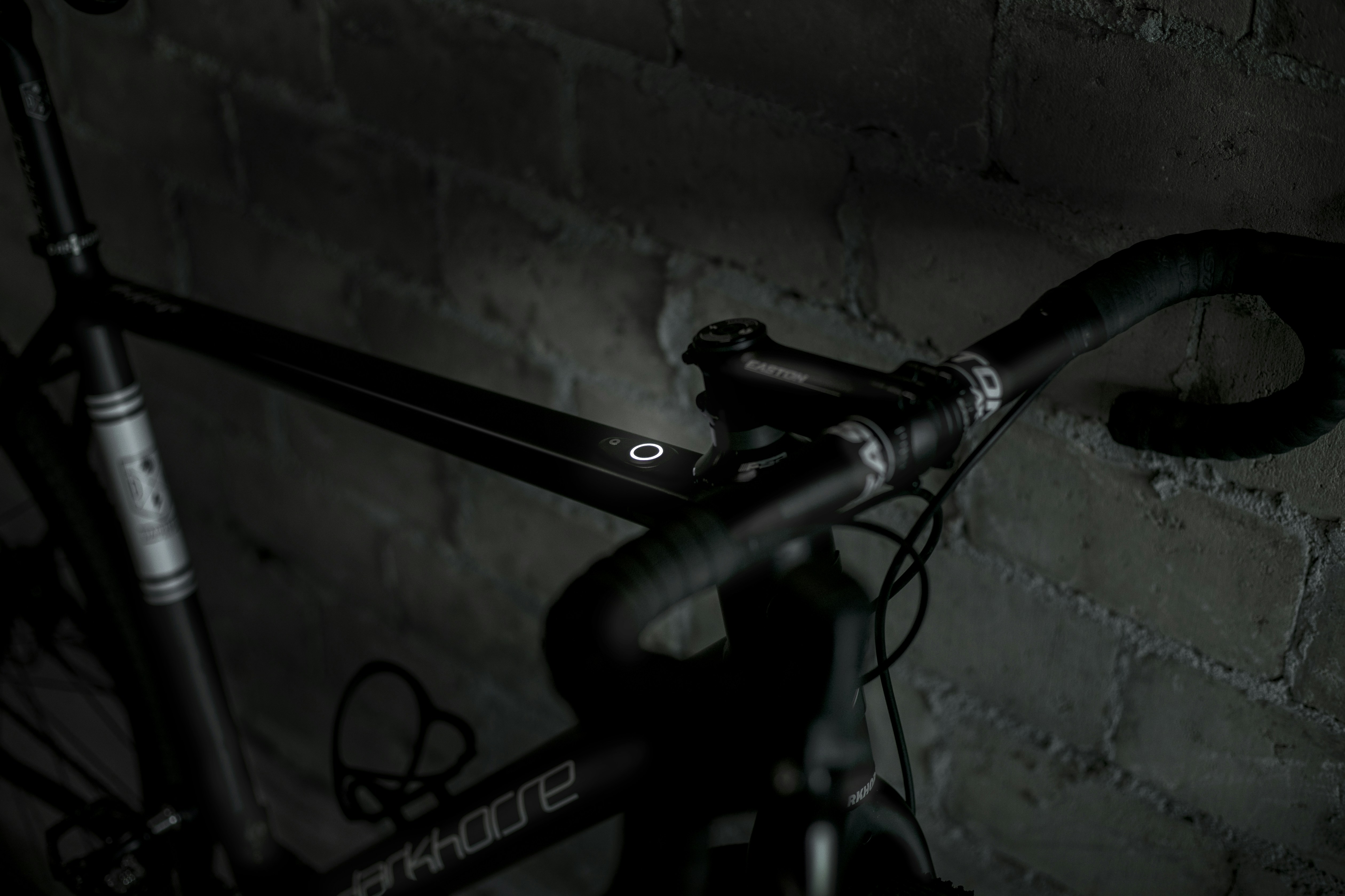 Shadowed Alloy: A Road Bike Quietly Reposes Against Brick in Low Light