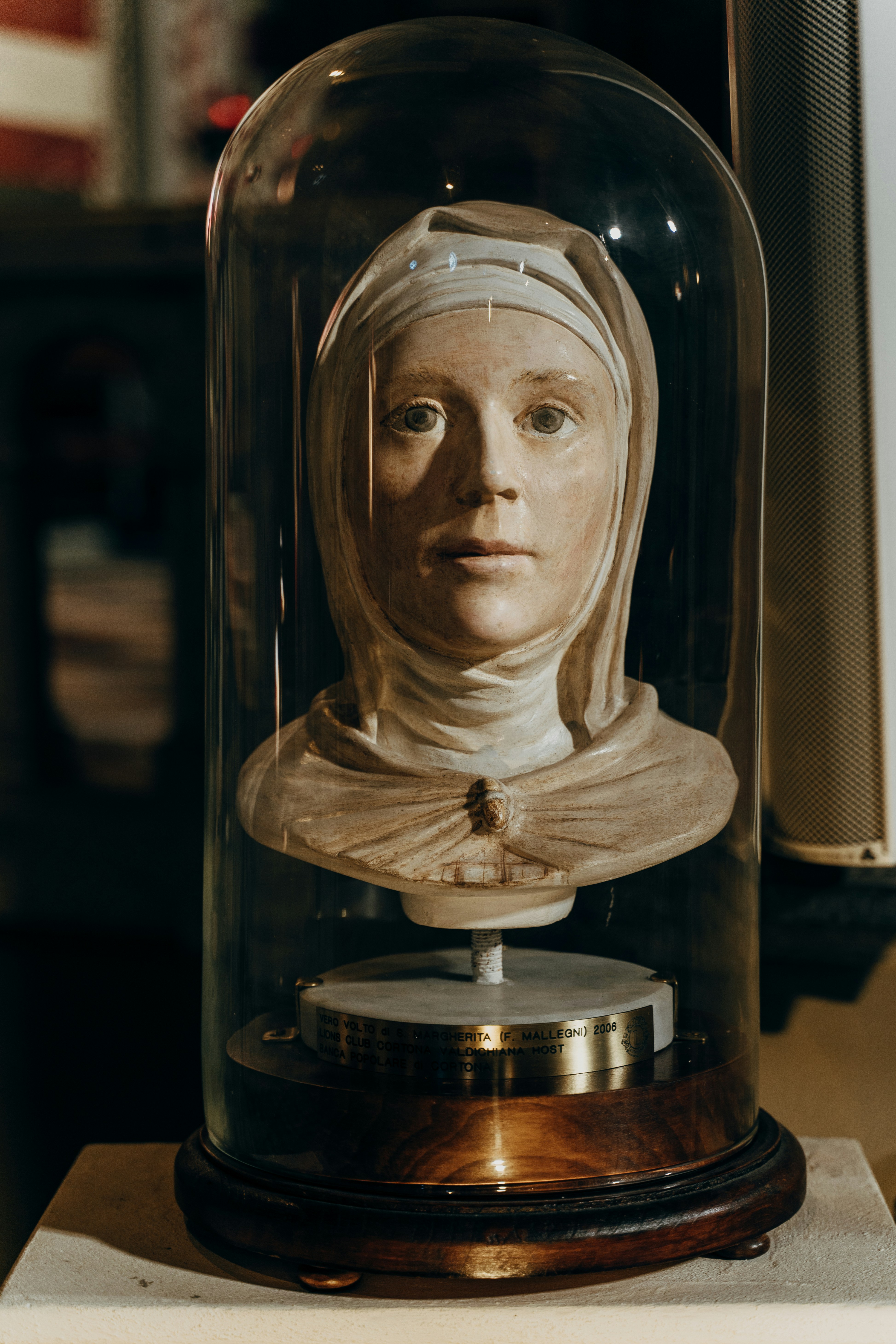 White ceramic bust of a veiled woman under a glass dome in soft, warm lighting.