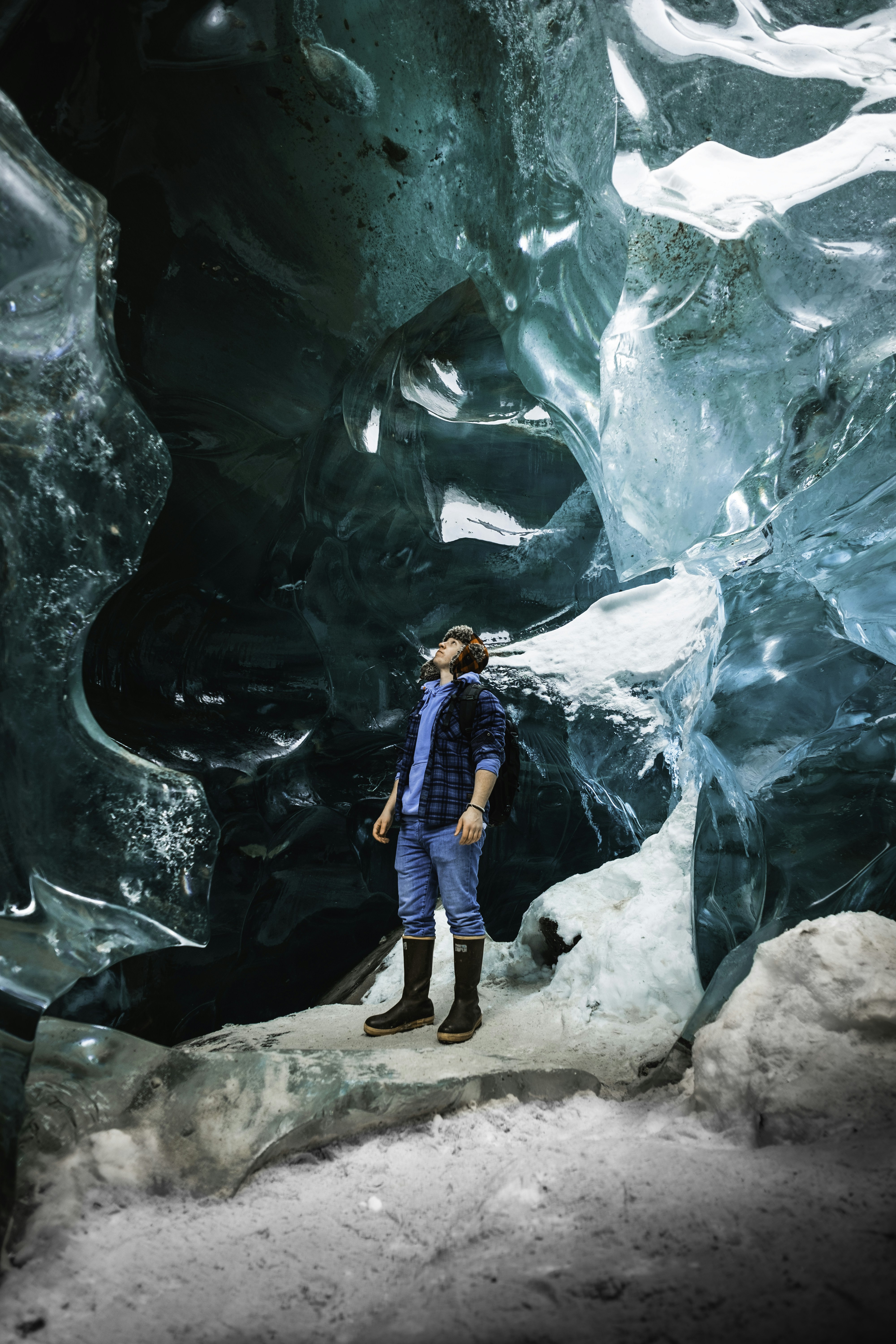Person in blue and black jacket standing on a rock inside a glistening ice cave in Juneau, Alaska.