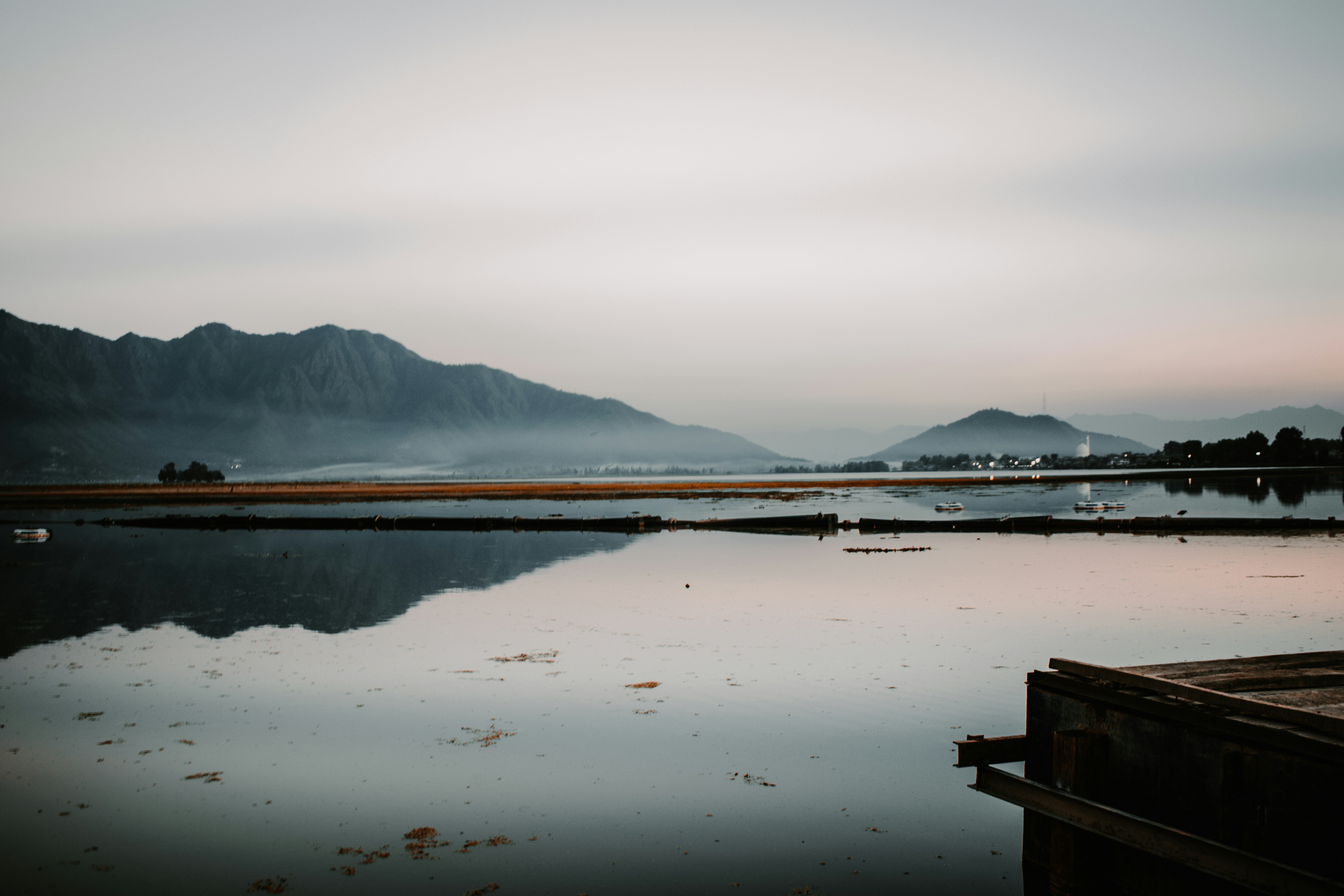 Tranquil lake reflecting distant mountains under a pastel sunrise sky.