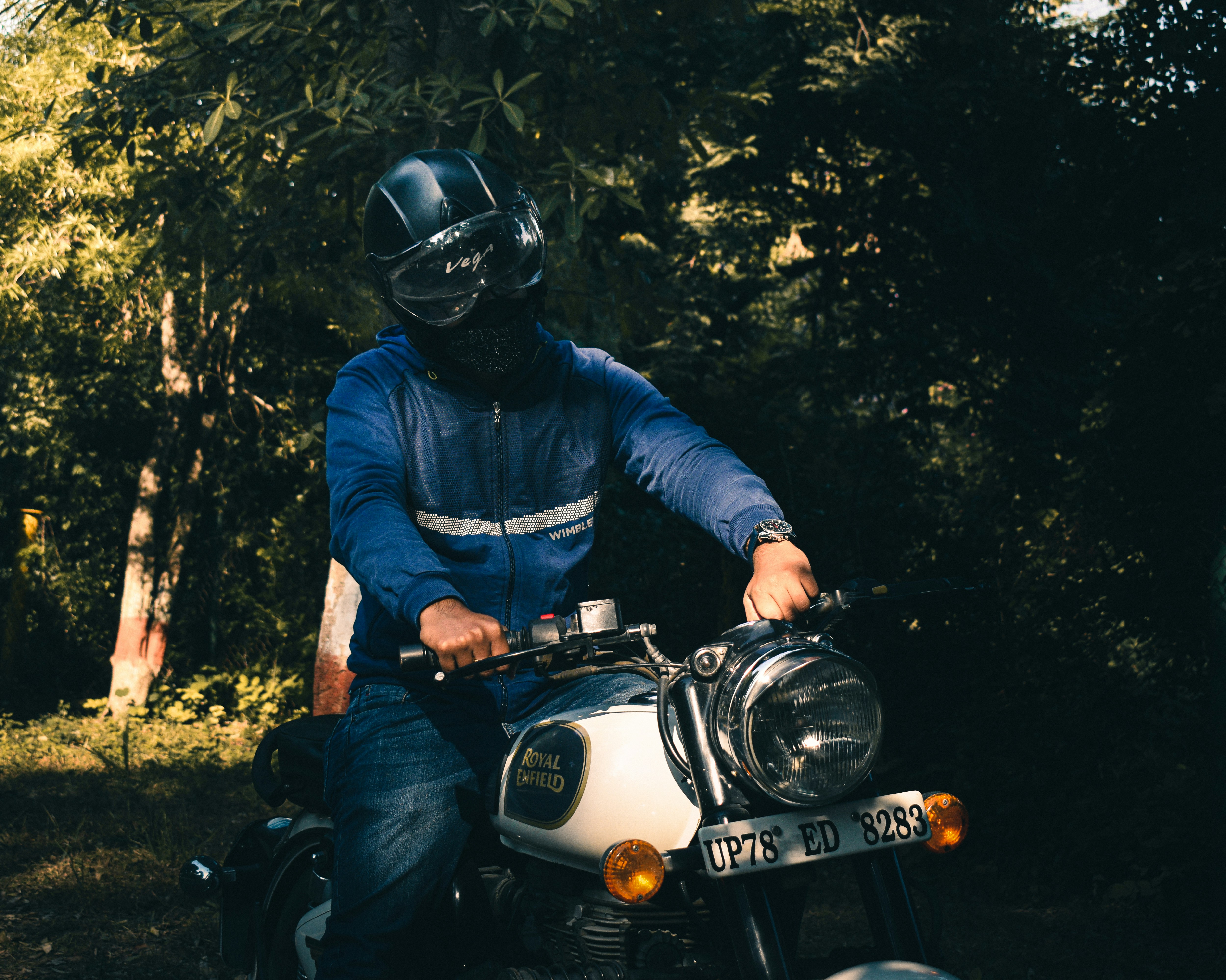 Motorcyclist in a blue jacket navigating a forest path under dappled sunlight.