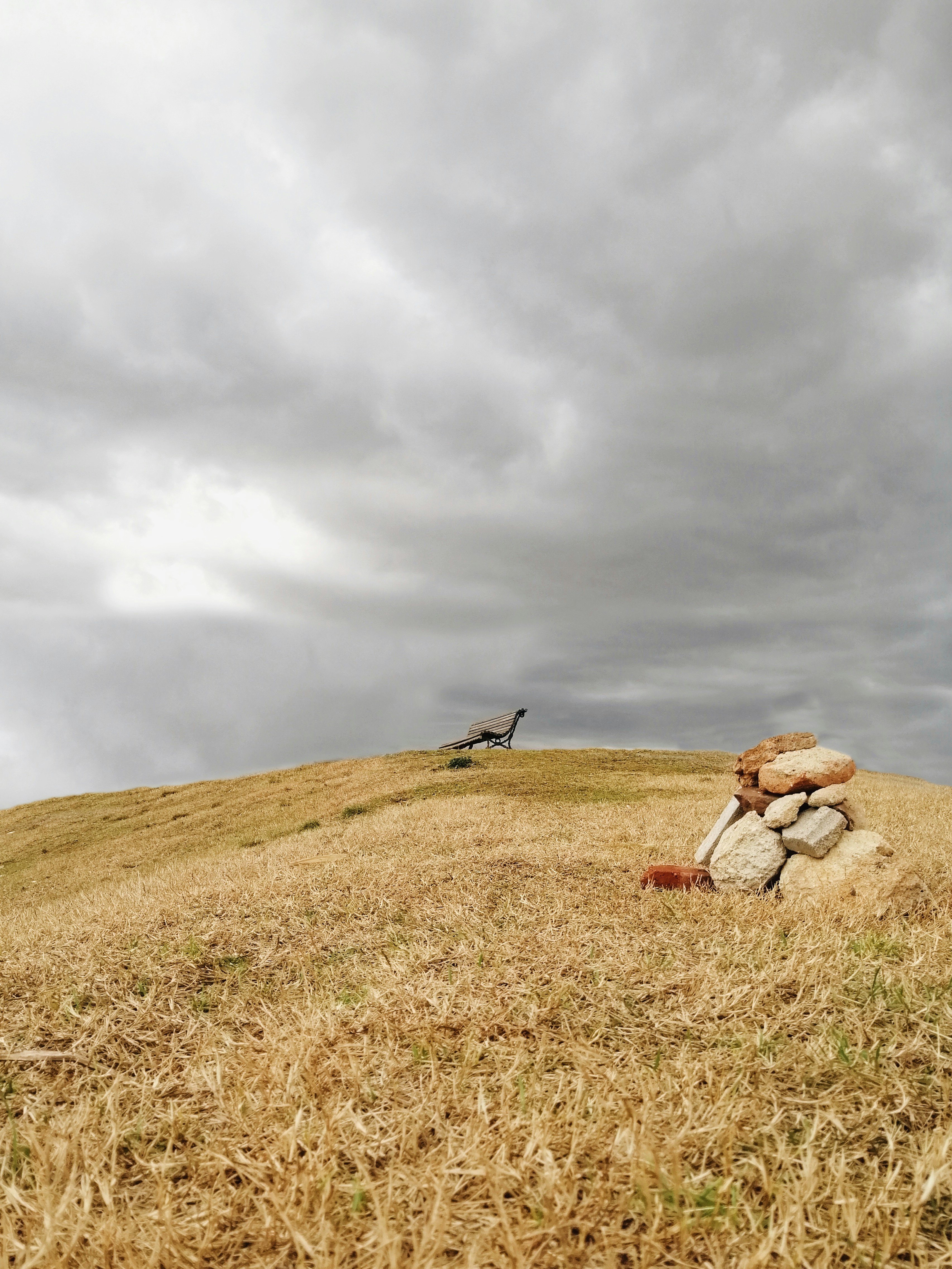 A solitary chair rests on a grassy hill under a dramatic sky, with a stone arrangement nearby. The scene captures a moment of tranquility amidst nature's grandeur.