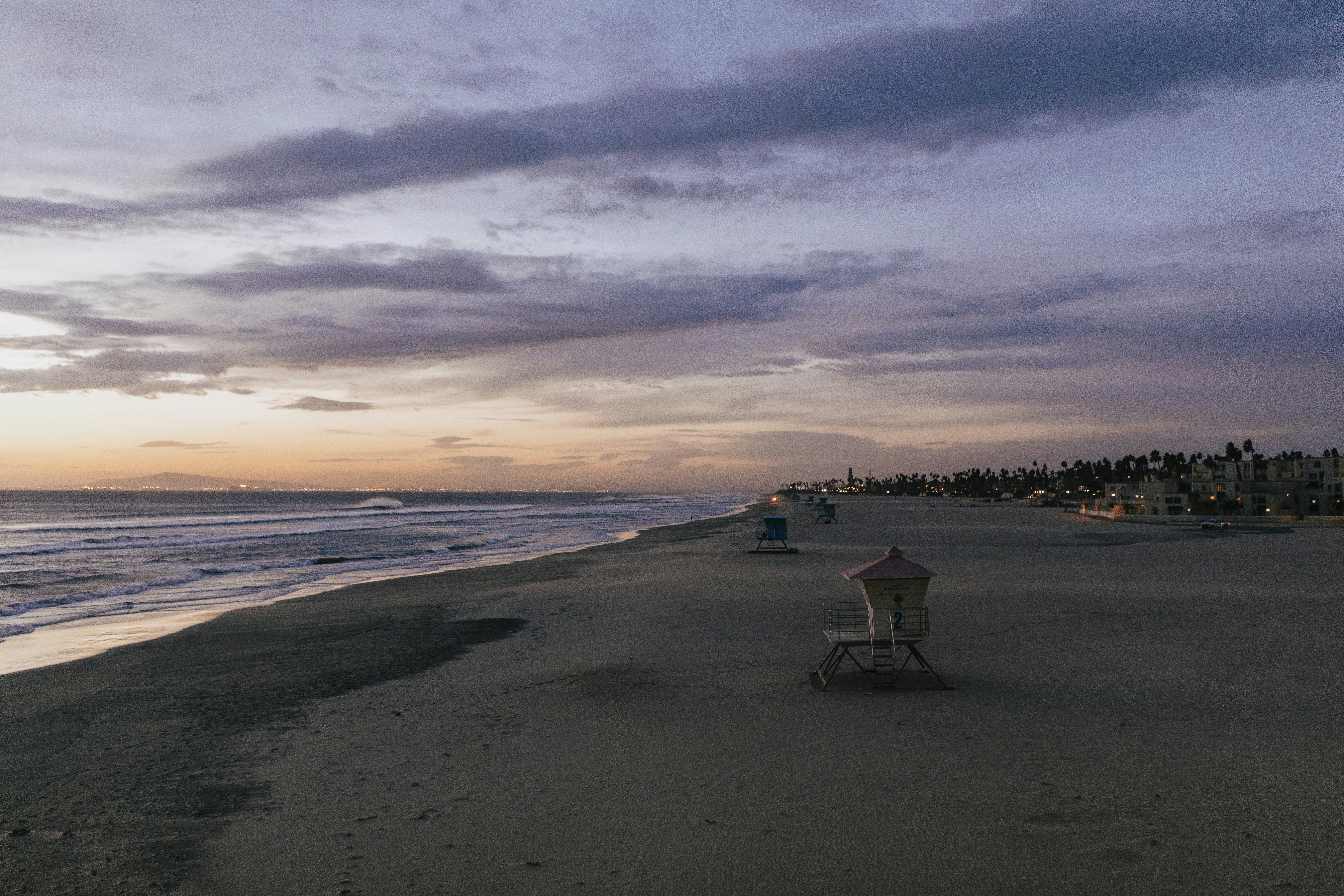 Quiet beach at dusk with a lifeguard tower and pastel sky reflecting on calm waves.