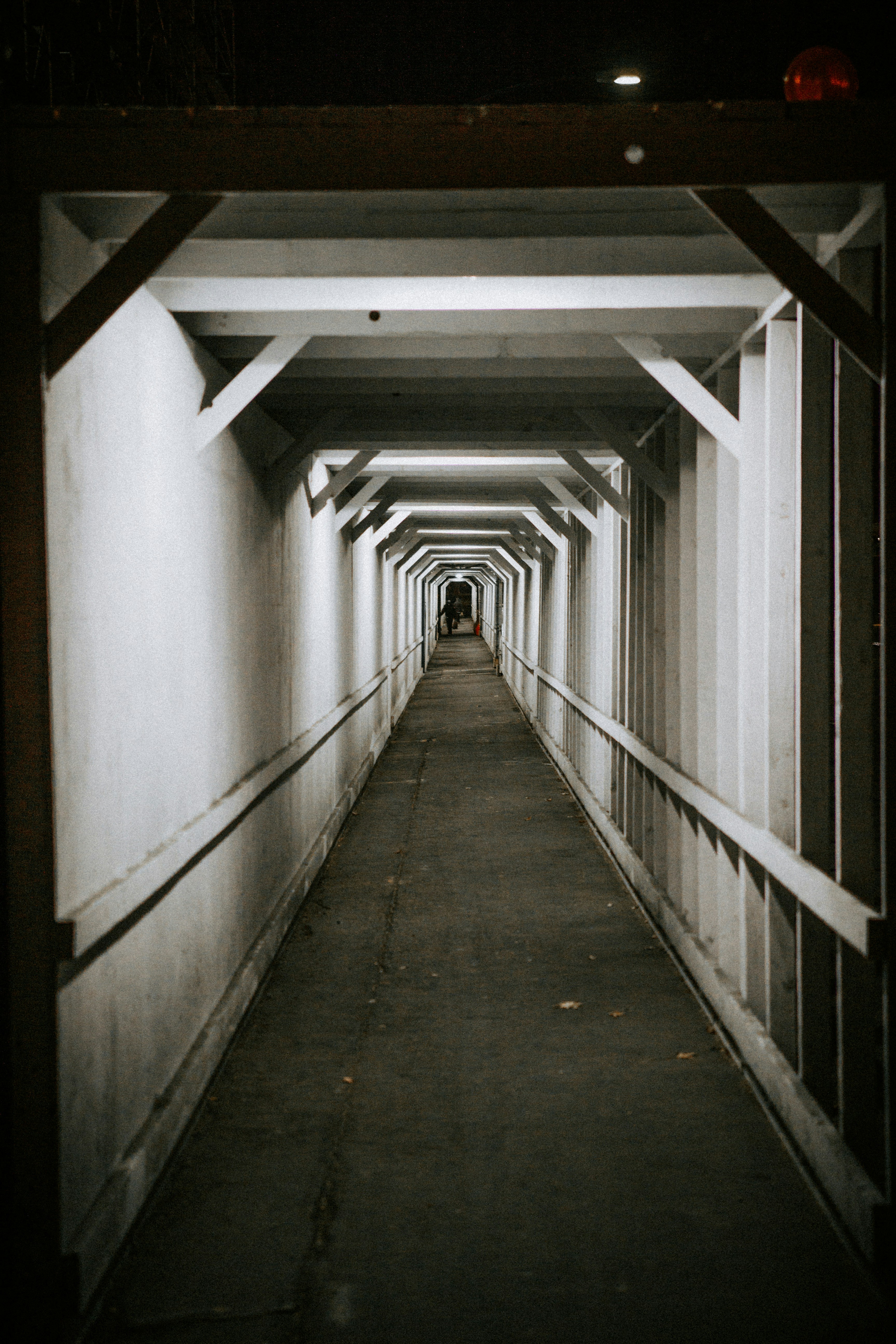 Illuminated corridor leading into darkness, framed by stark white walls and structural beams.