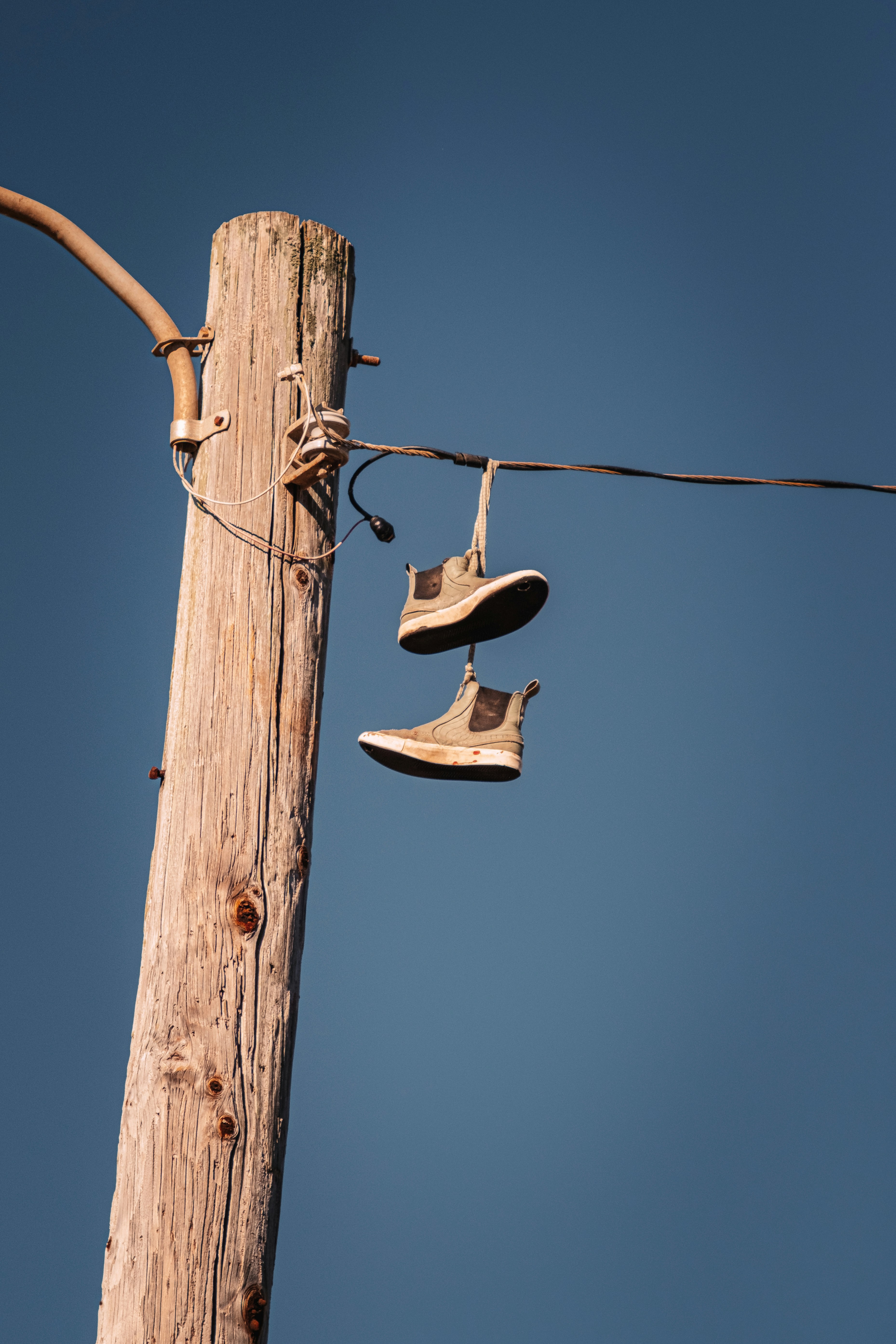 Hanging Shoes on a Weathered Pole Against a Clear Blue Sky