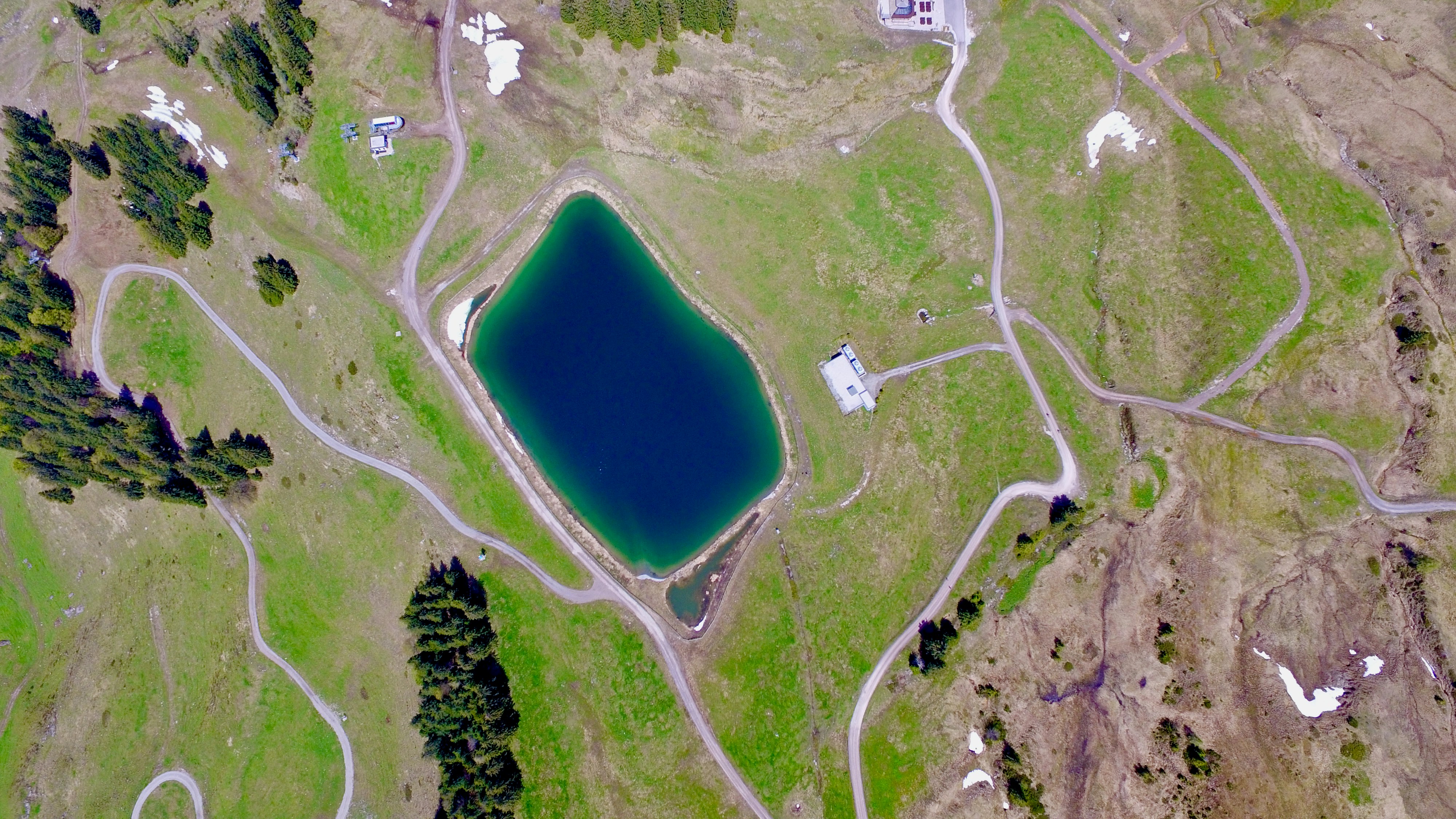 Aerial view of a turquoise lake surrounded by winding paths and grassy slopes in a park-like landscape.