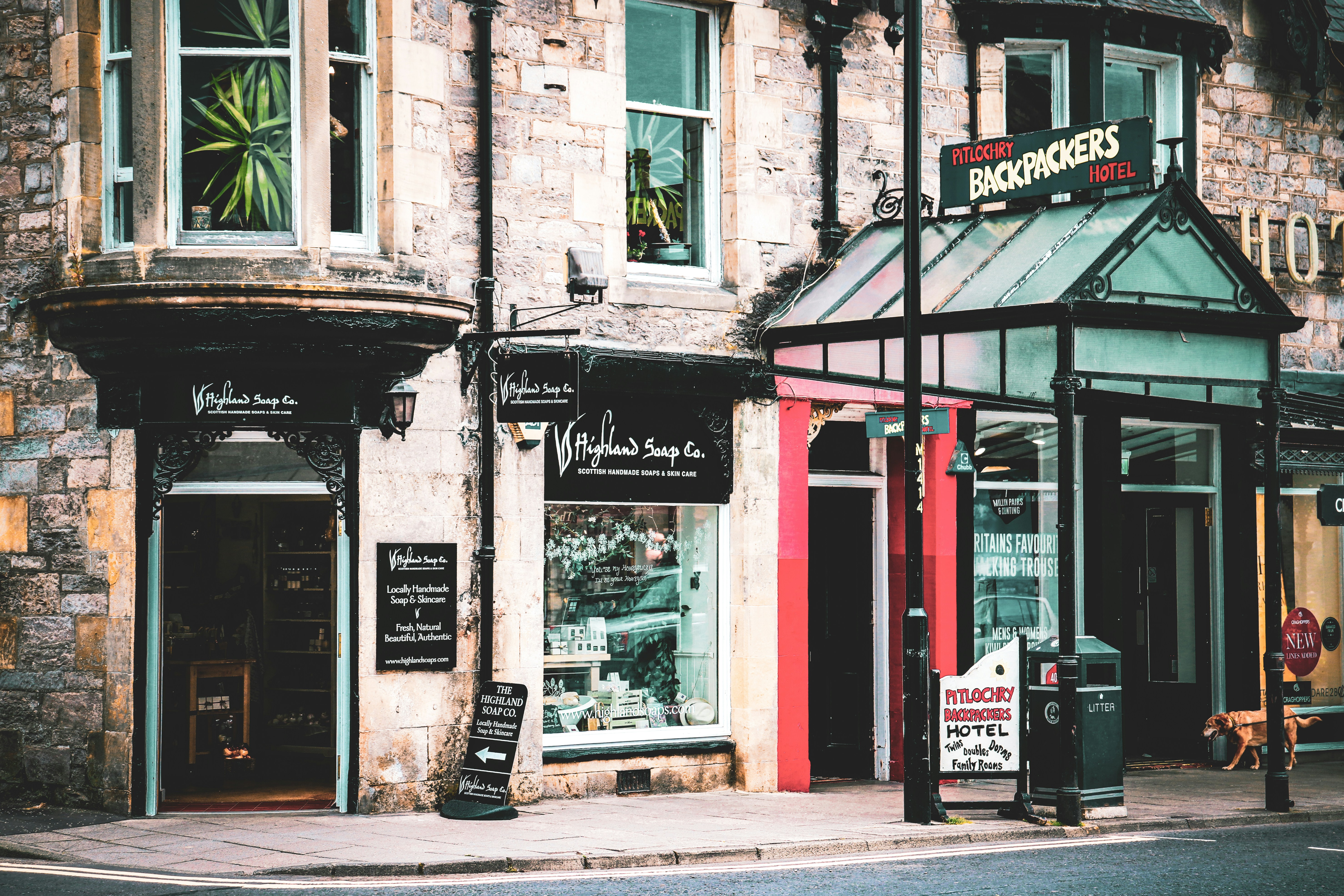 Quaint storefronts showcasing local shops and a backpackers' hotel in a historic stone building. The vibrant colors and signage invite exploration.