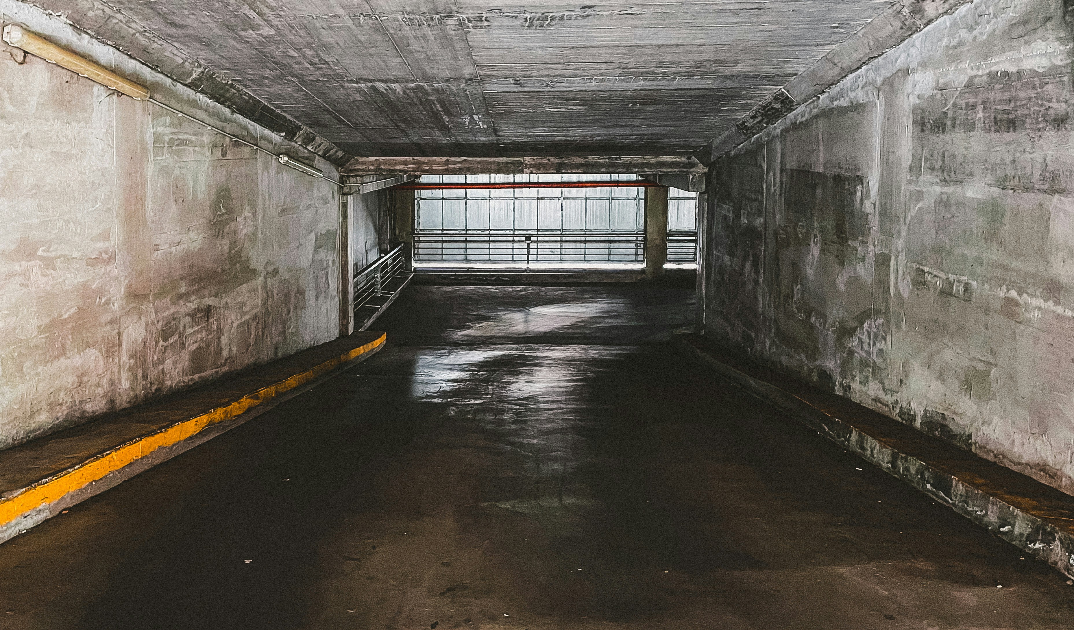 Dimly lit parking garage with a smooth, reflective surface and a yellow line guiding the way. The distant light creates a sense of depth and mystery.