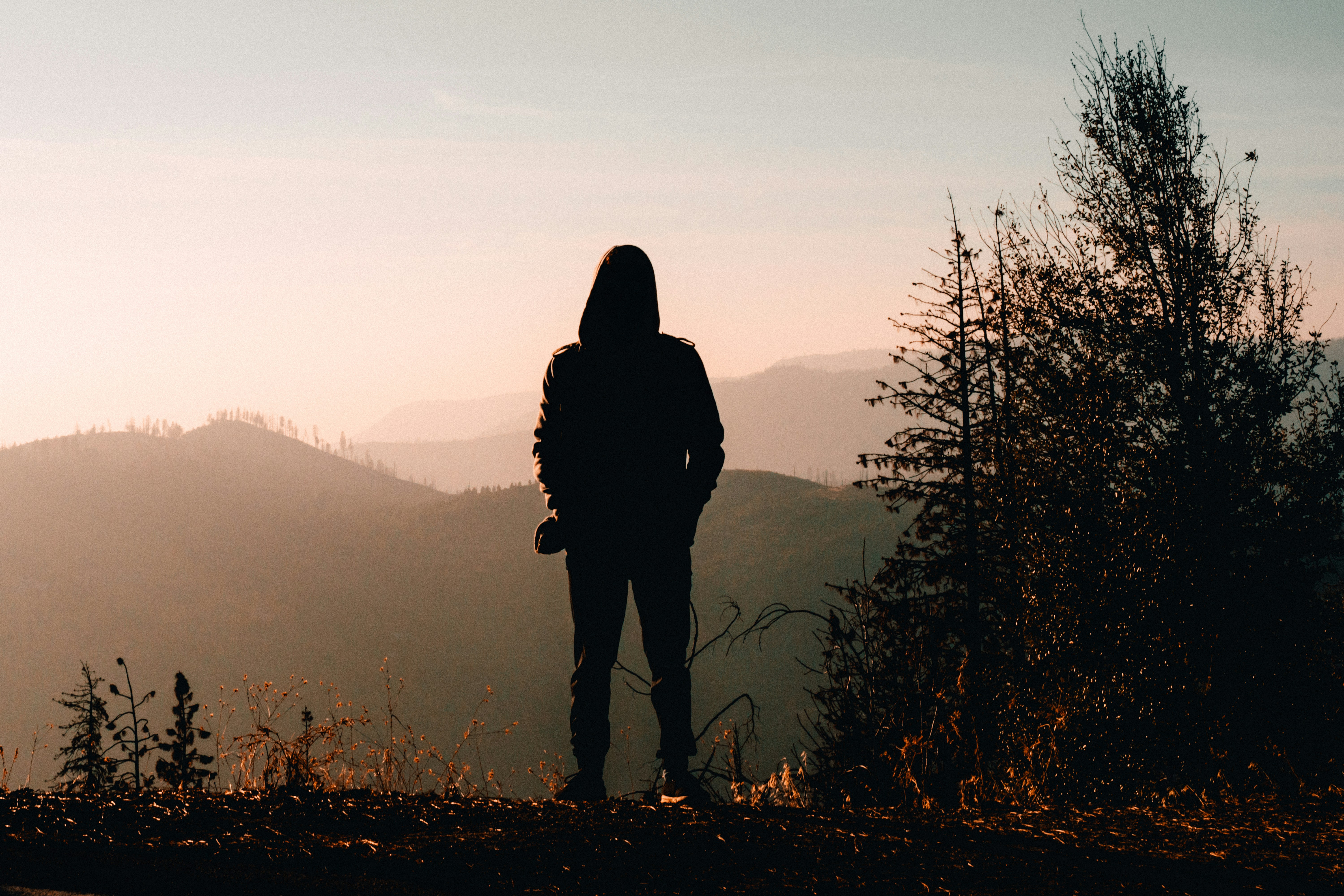 Silhouette of a person standing on a ridge, overlooking misty mountains at sunset. The scene captures a moment of reflection and tranquility.