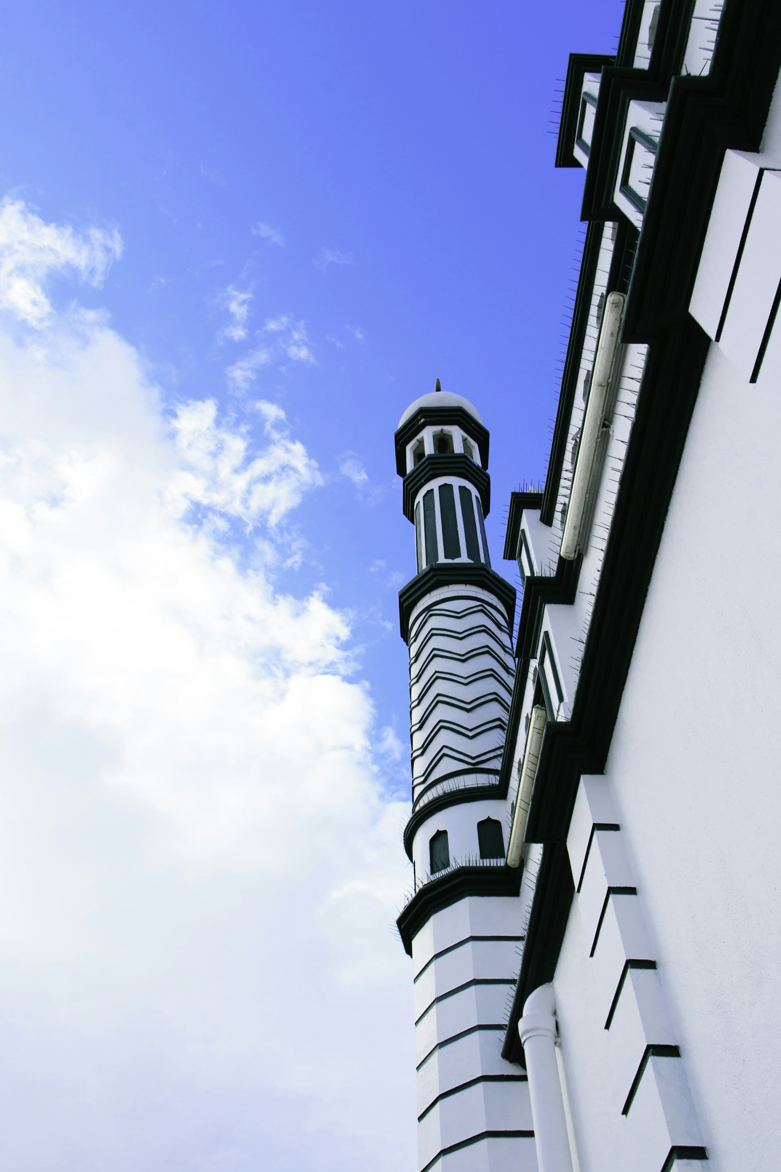 A striking minaret rises against a bright blue sky, showcasing intricate architectural details and bold lines. The contrast between the white structure and the vibrant backdrop emphasizes its grandeur.