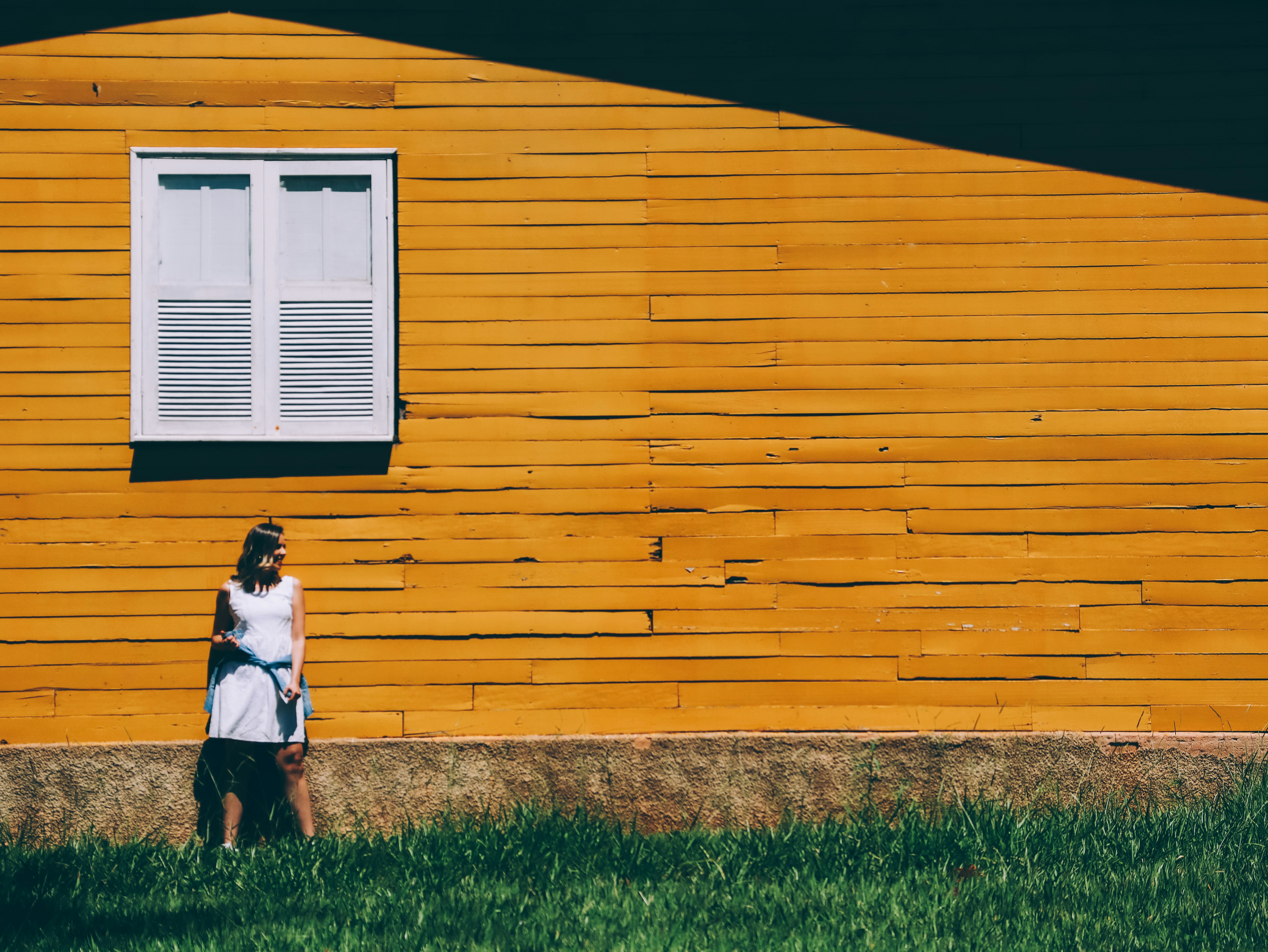Woman in a white dress at the base of a bright yellow wall