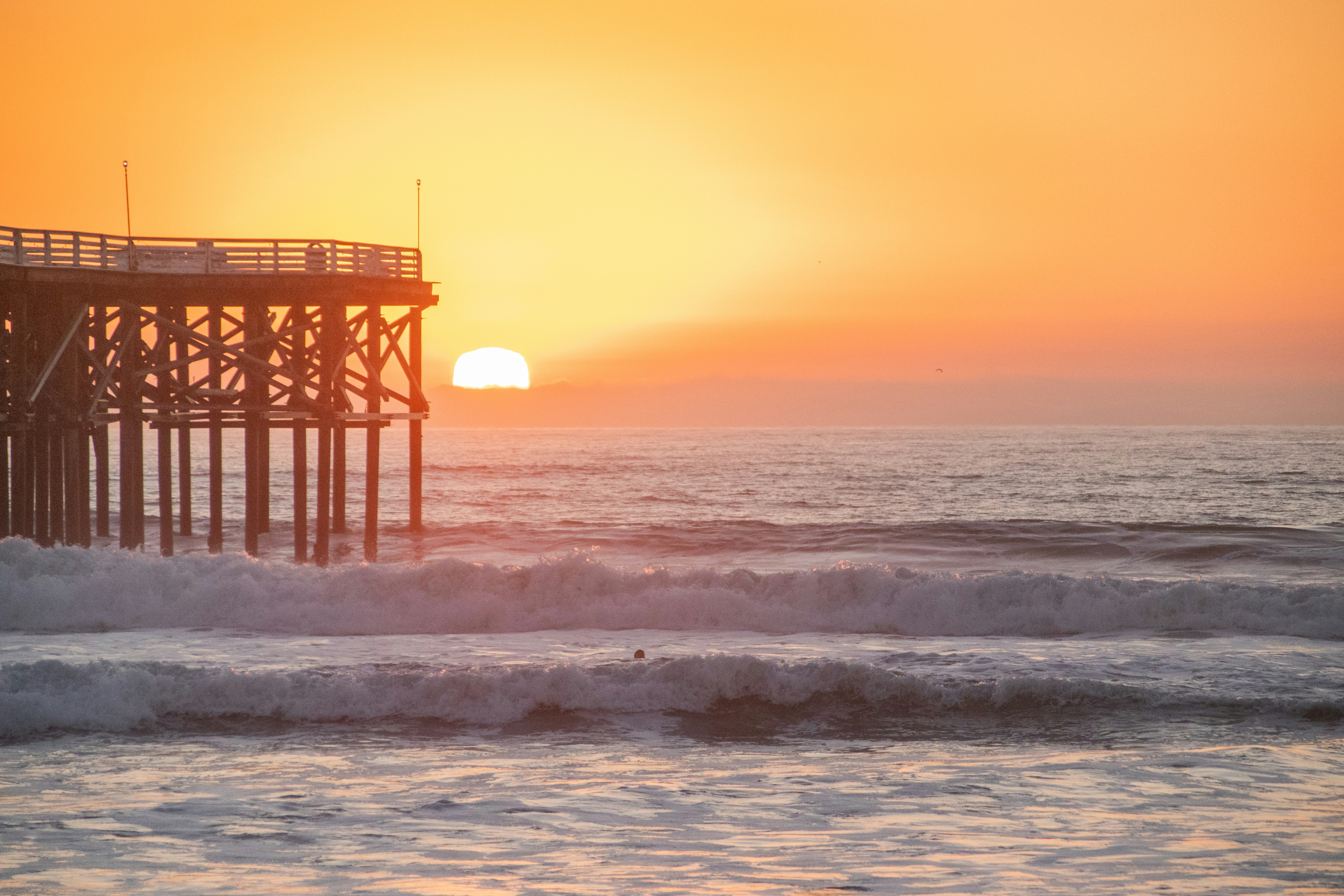 Wooden pier extending into the ocean with vibrant sunset hues on the horizon.