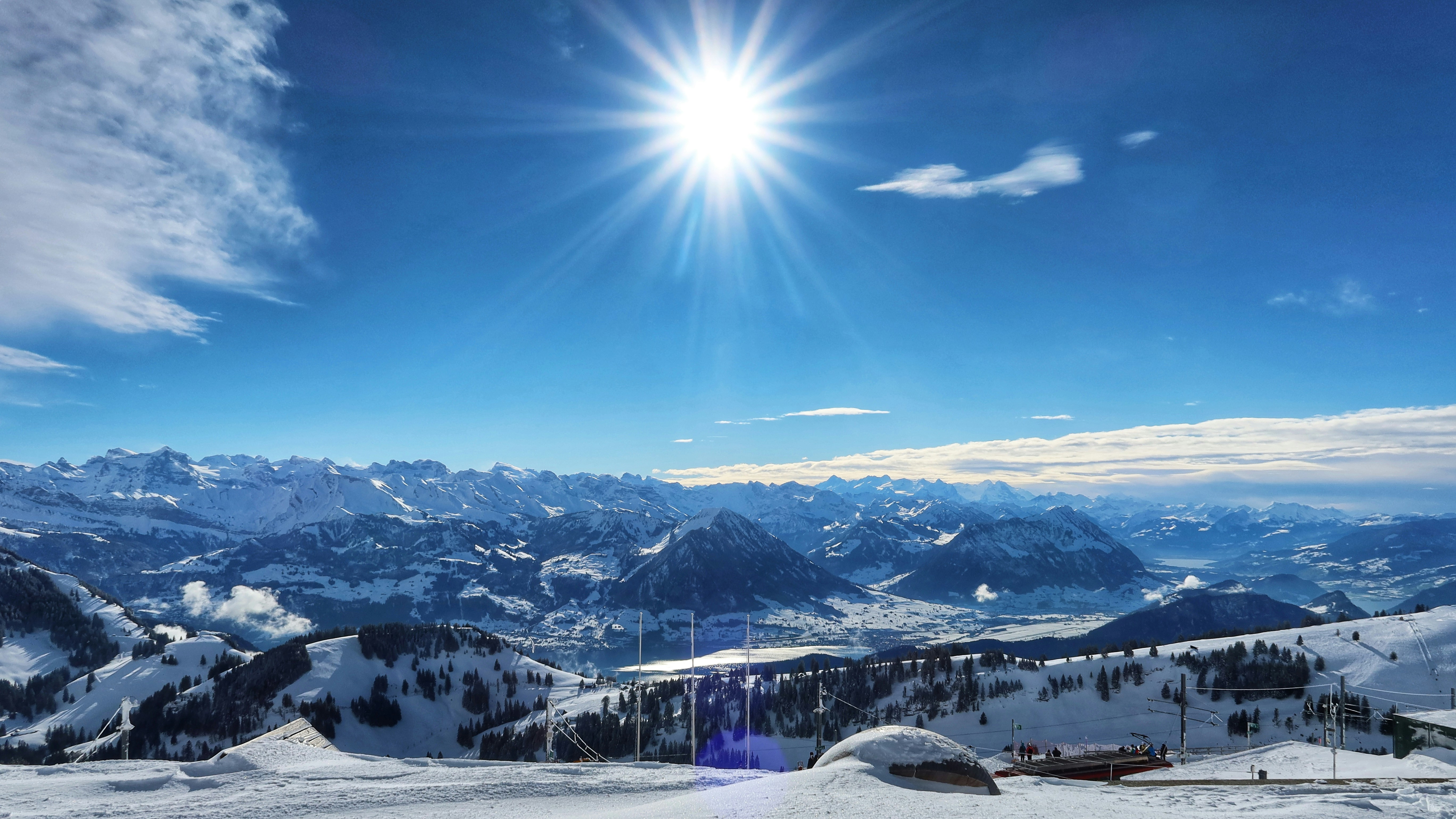 Snow-covered mountains stretch across the horizon, illuminated by a brilliant sun casting rays over the landscape. The scene captures the serene beauty of a winter day.