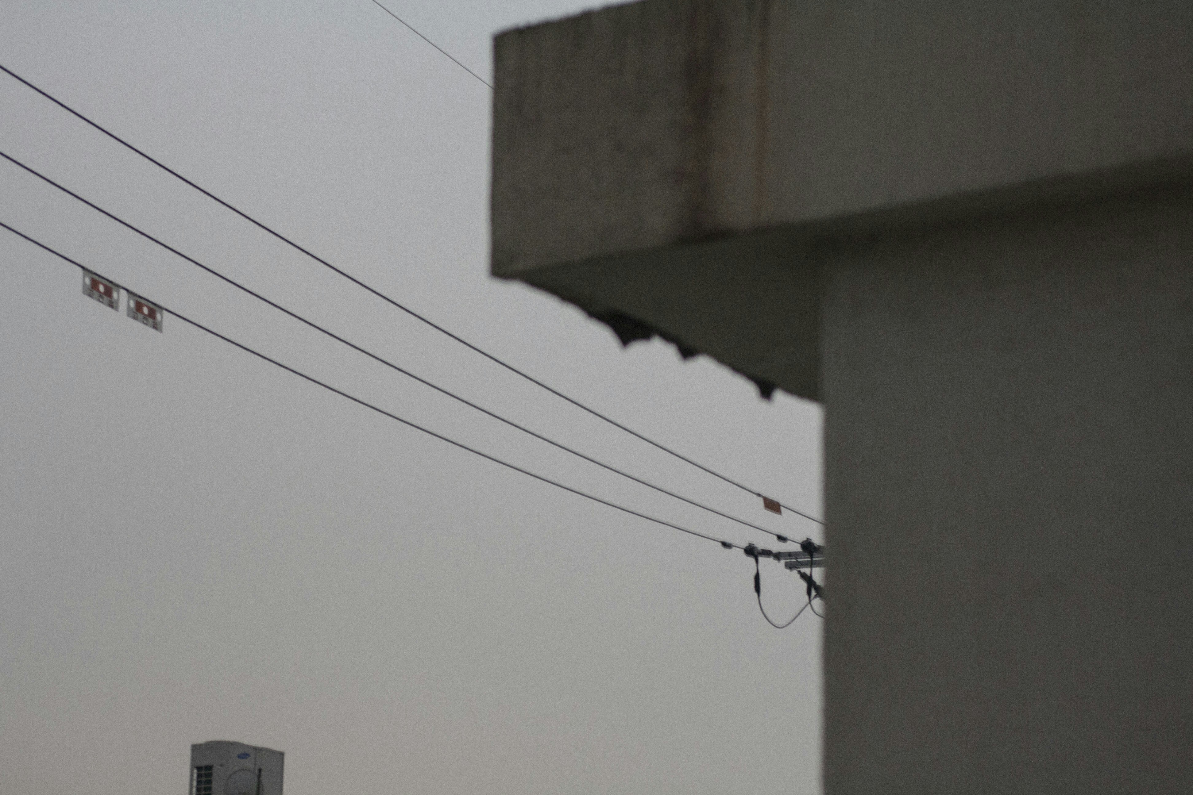 Electrical wires intersect against a muted sky, framed by the edge of a building. The composition hints at urban life and the unseen connections that power it.