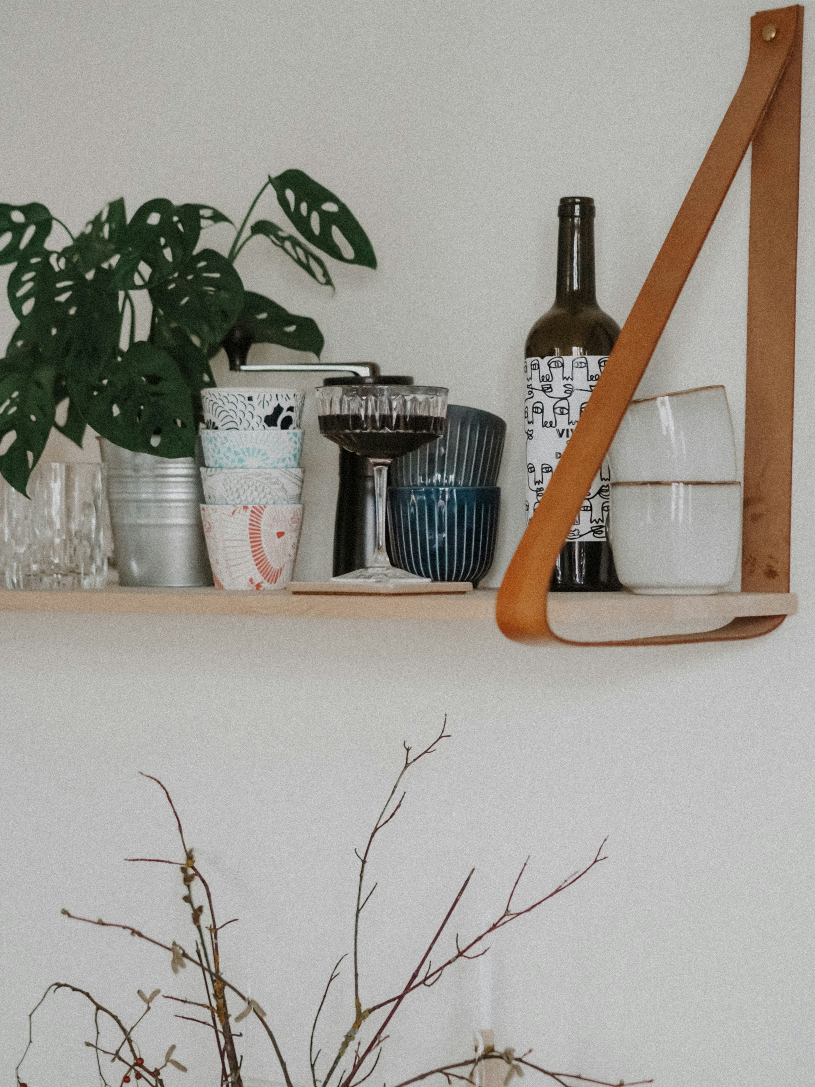 Stylish shelf arrangement showcasing colorful cups, a wine bottle, and a vibrant plant, blending functionality with aesthetics.