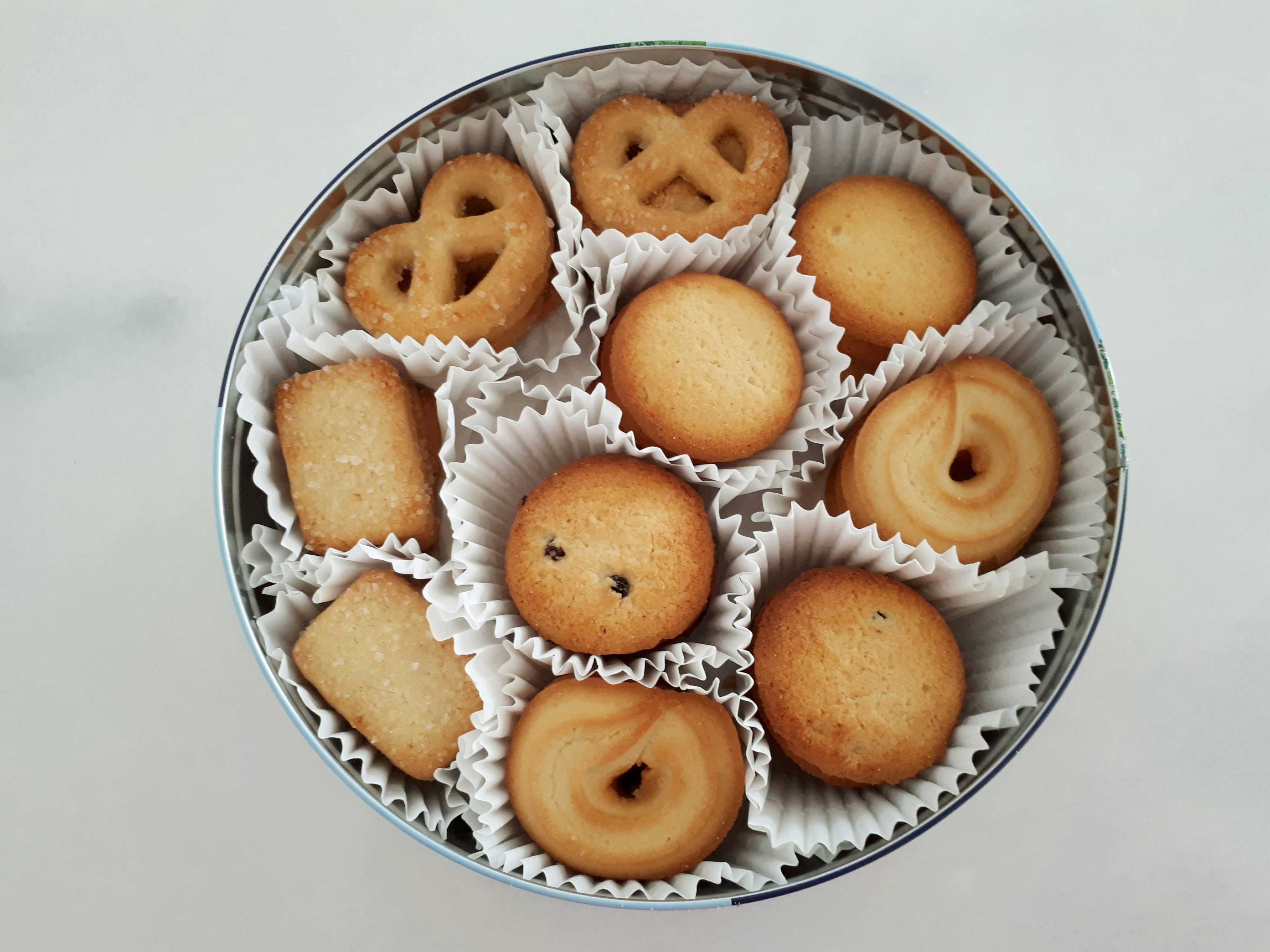 Assorted baked treats arranged neatly in a decorative tin, each nestled in paper liners, showcasing a variety of shapes and textures.