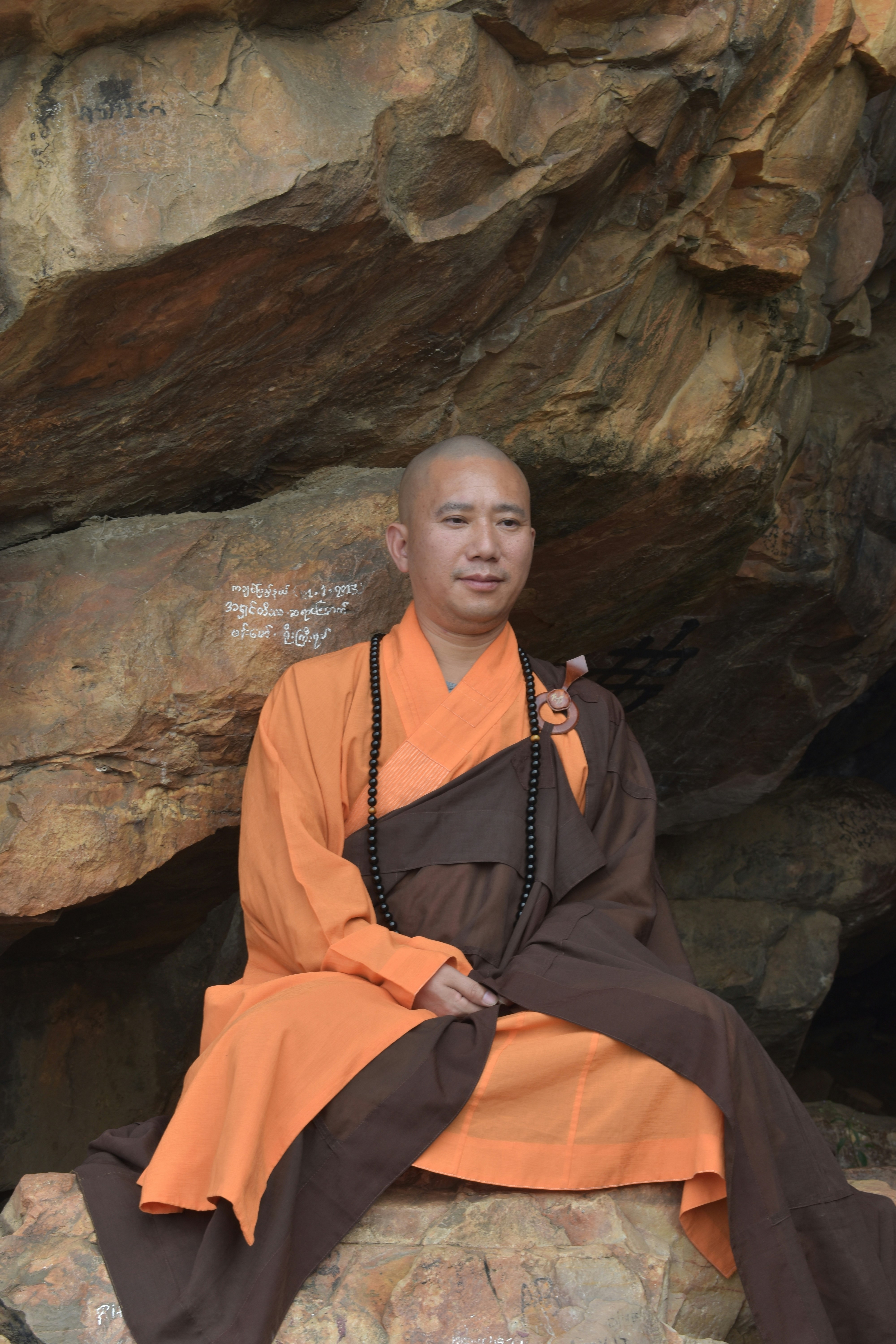 A monk in traditional attire sits serenely against a rocky backdrop, embodying tranquility and contemplation.