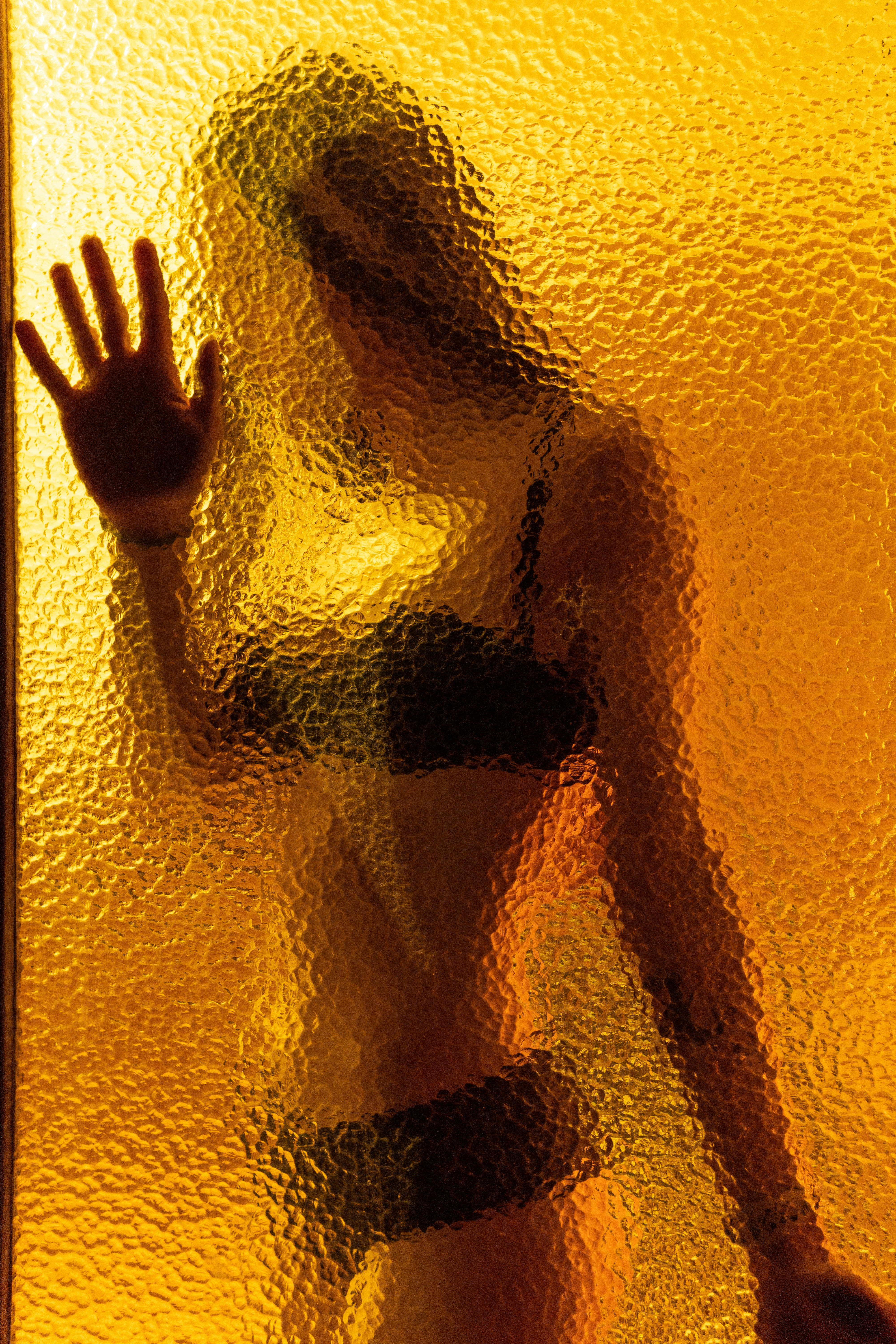 Silhouette of a figure pressing against a textured golden surface, creating an ethereal effect.