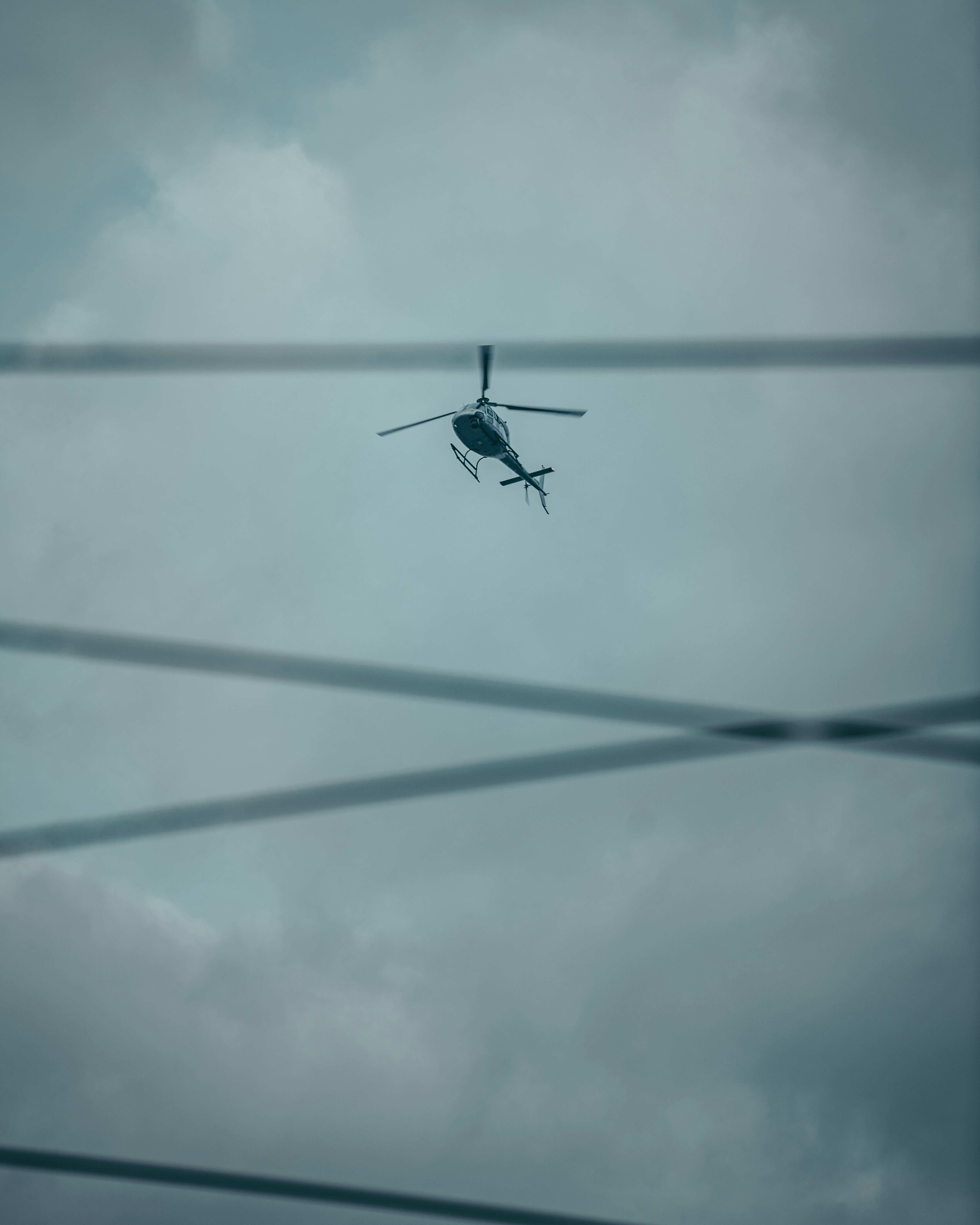 Helicopter Between Wires: An aerial silhouette threading diagonal cables beneath a moody sky