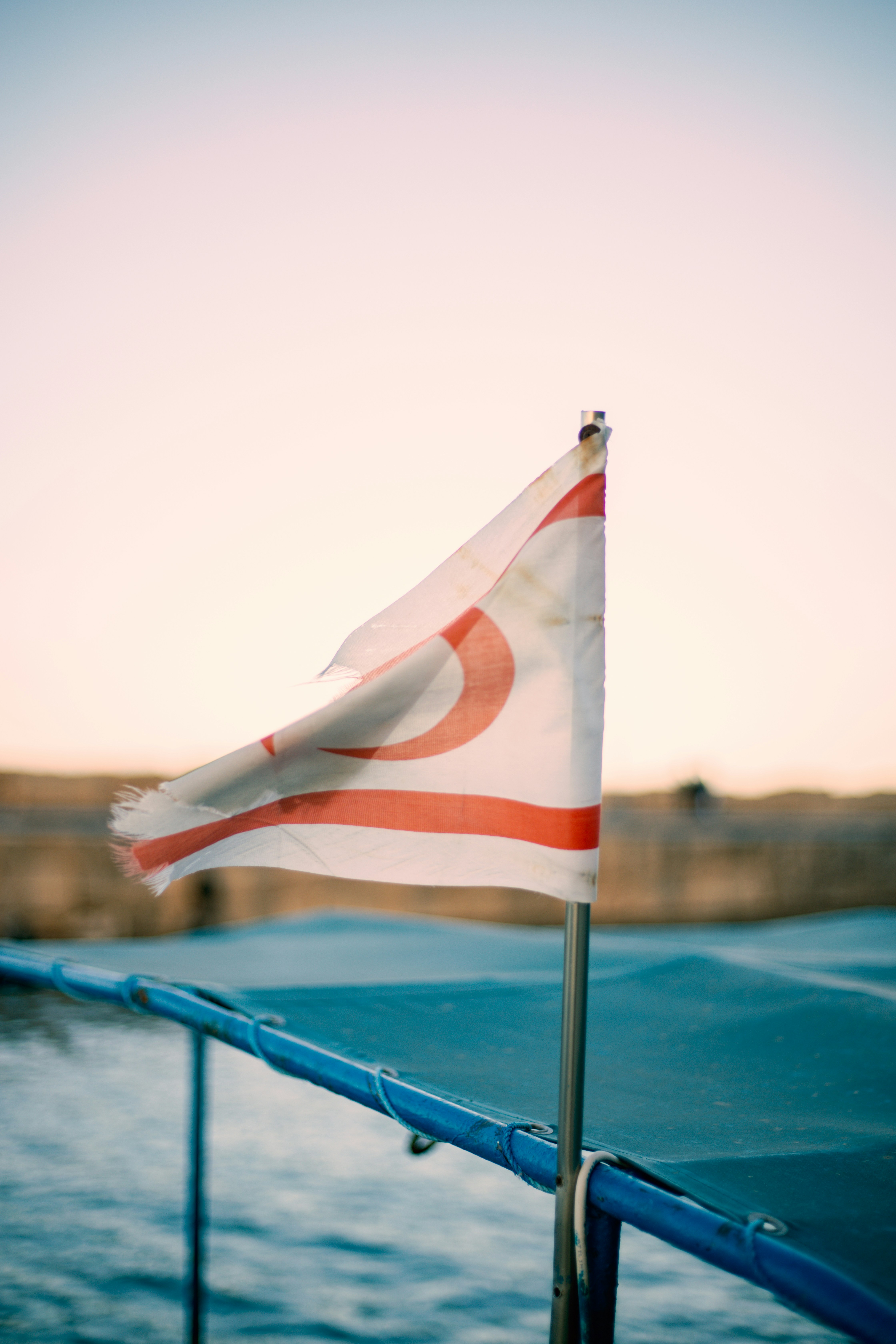 Tattered flag fluttering atop a boat, catching the soft hues of dusk over calm waters.